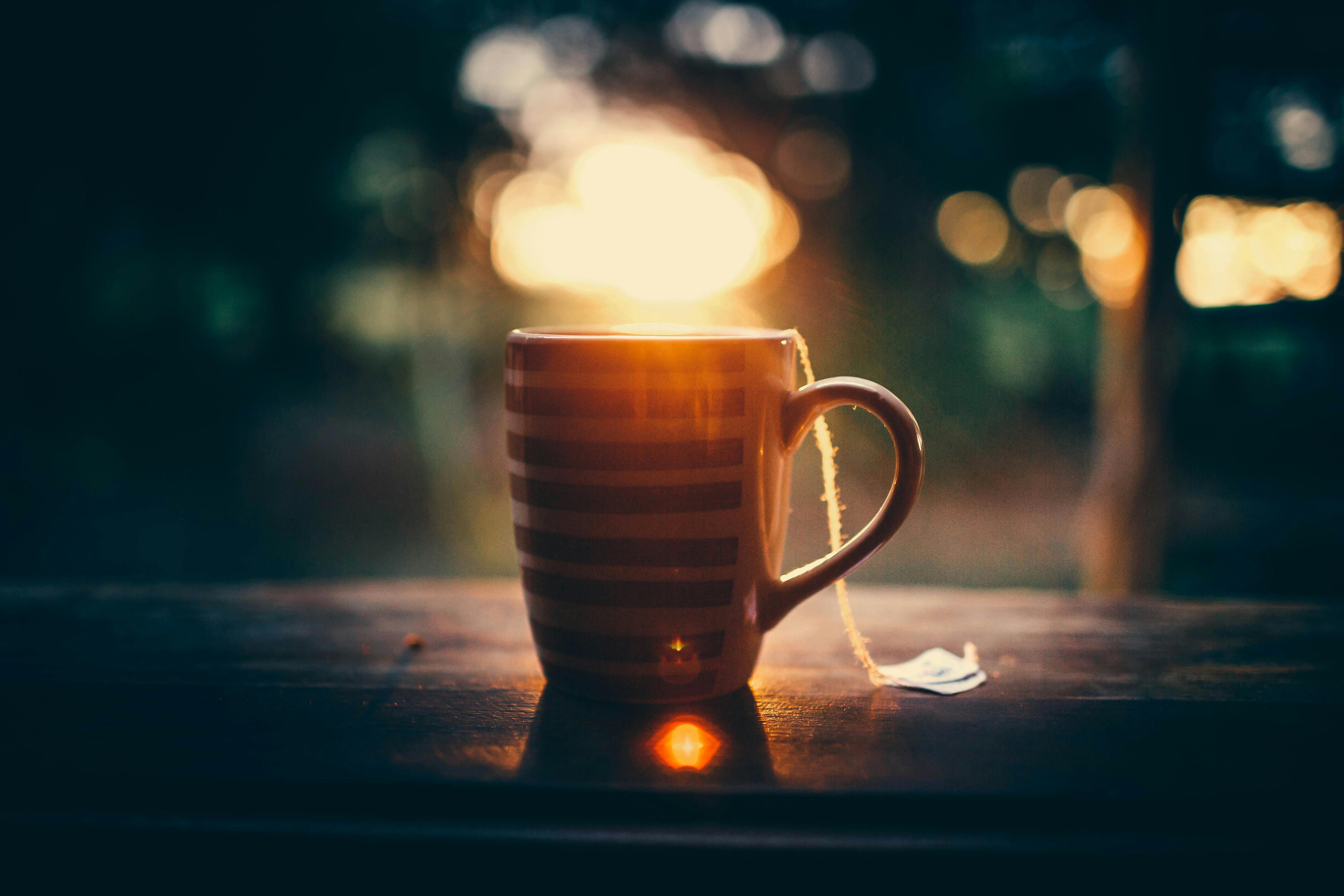 Mug of aromatic hot tea on wooden surface against blurred green forest ...