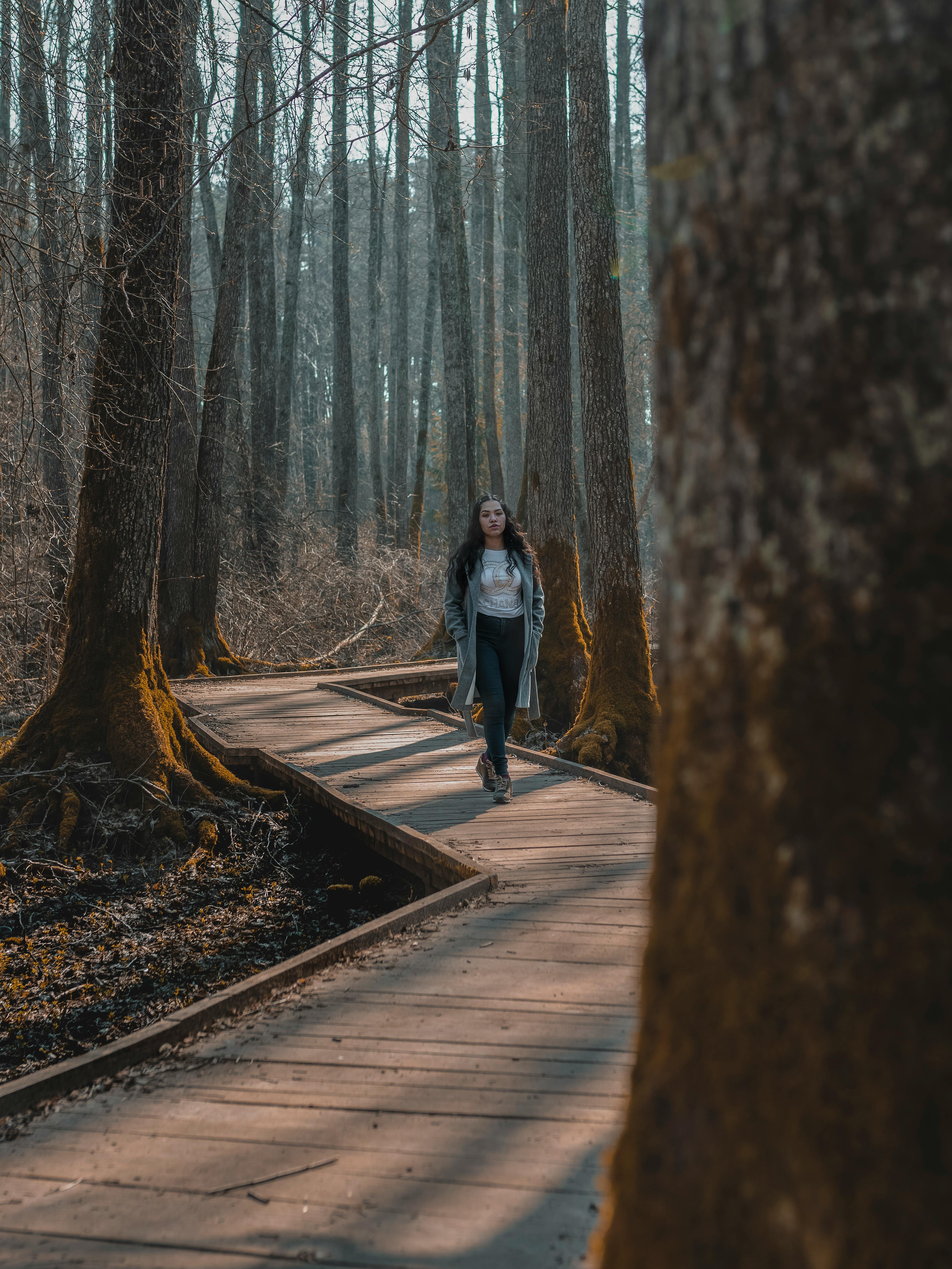 Woman Walking on Wooden Pathway Between Trees · Free Stock Photo