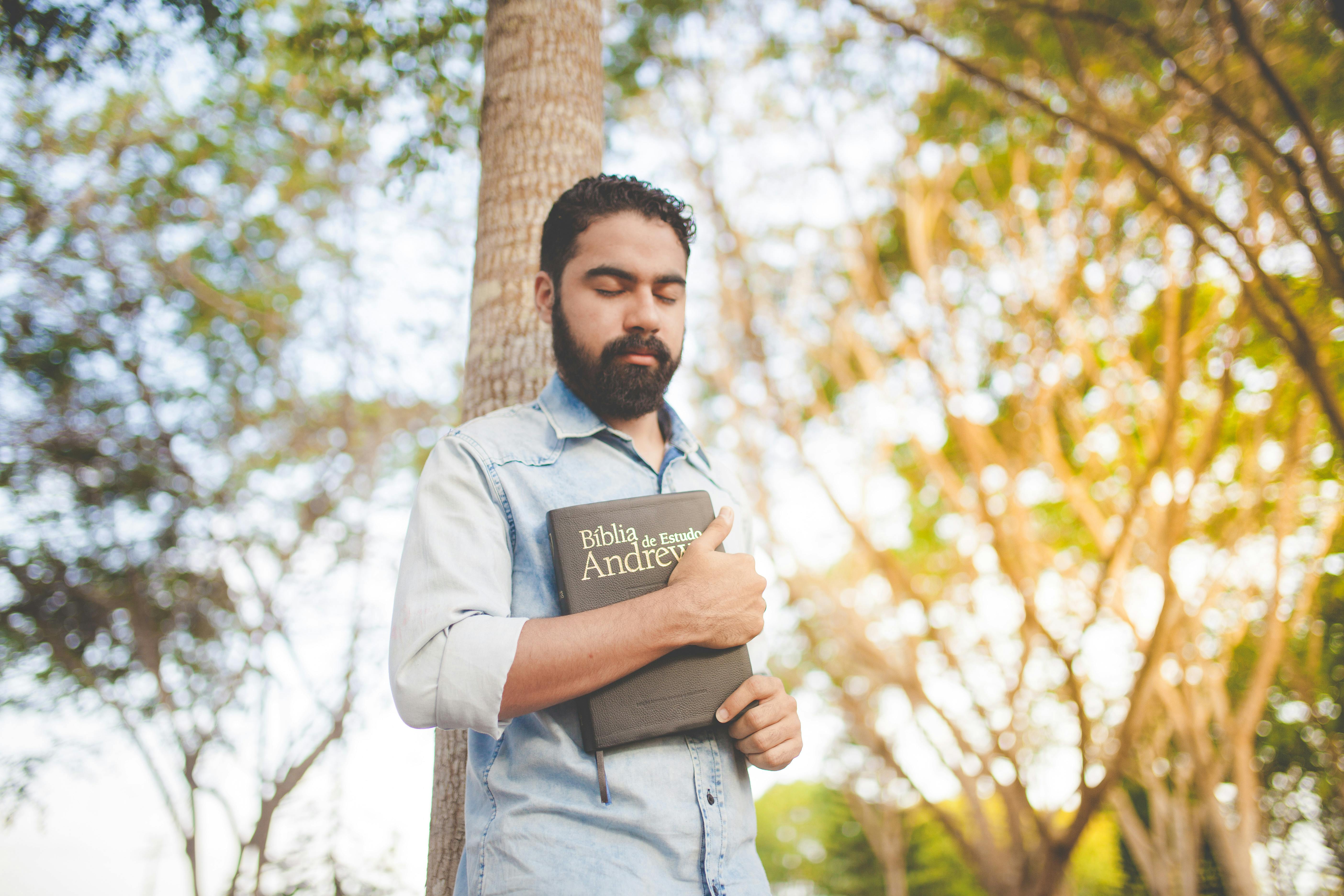 Man Holding a Bible While Praying · Free Stock Photo