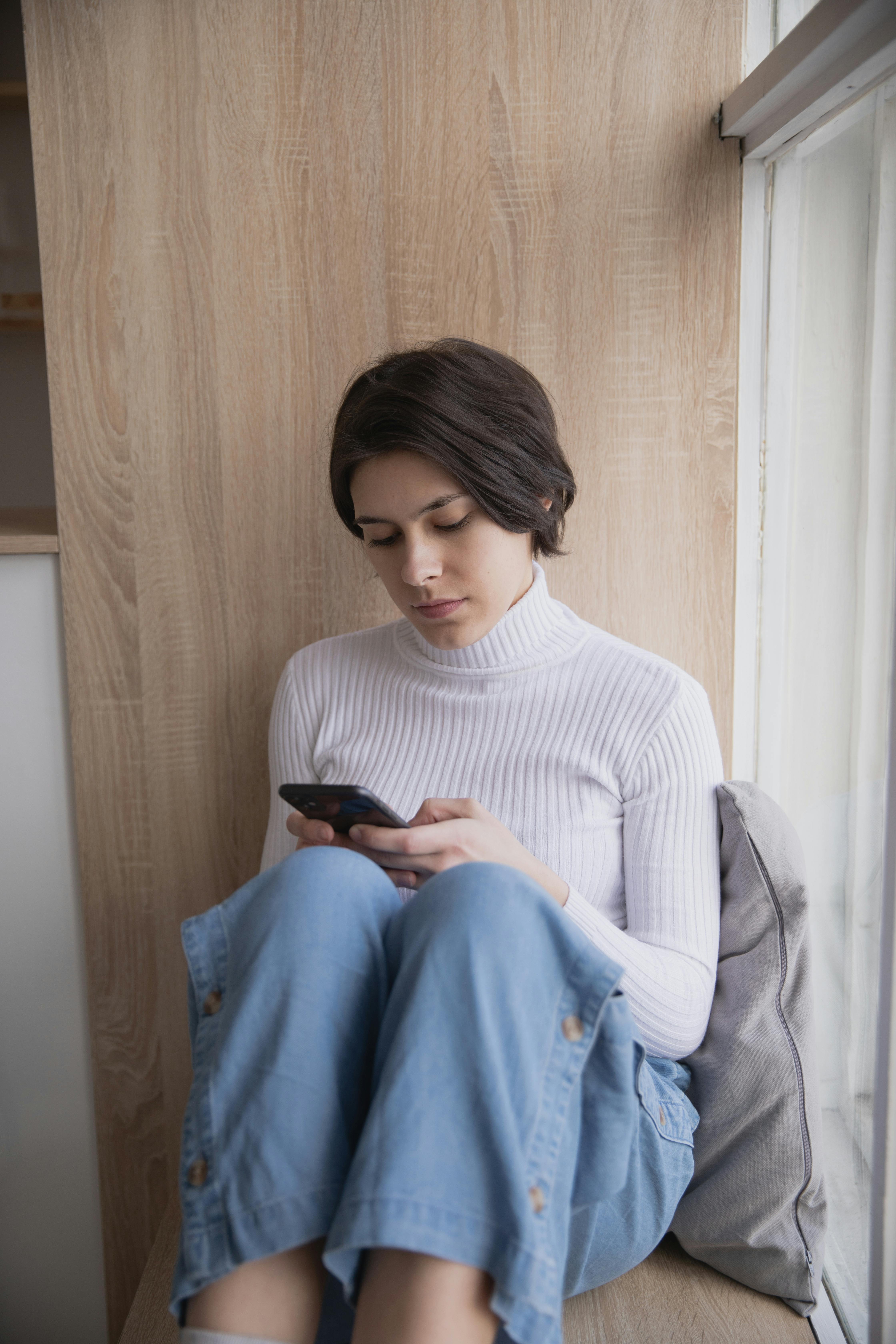 Woman Sitting Beside Window Holding Phone · Free Stock Photo