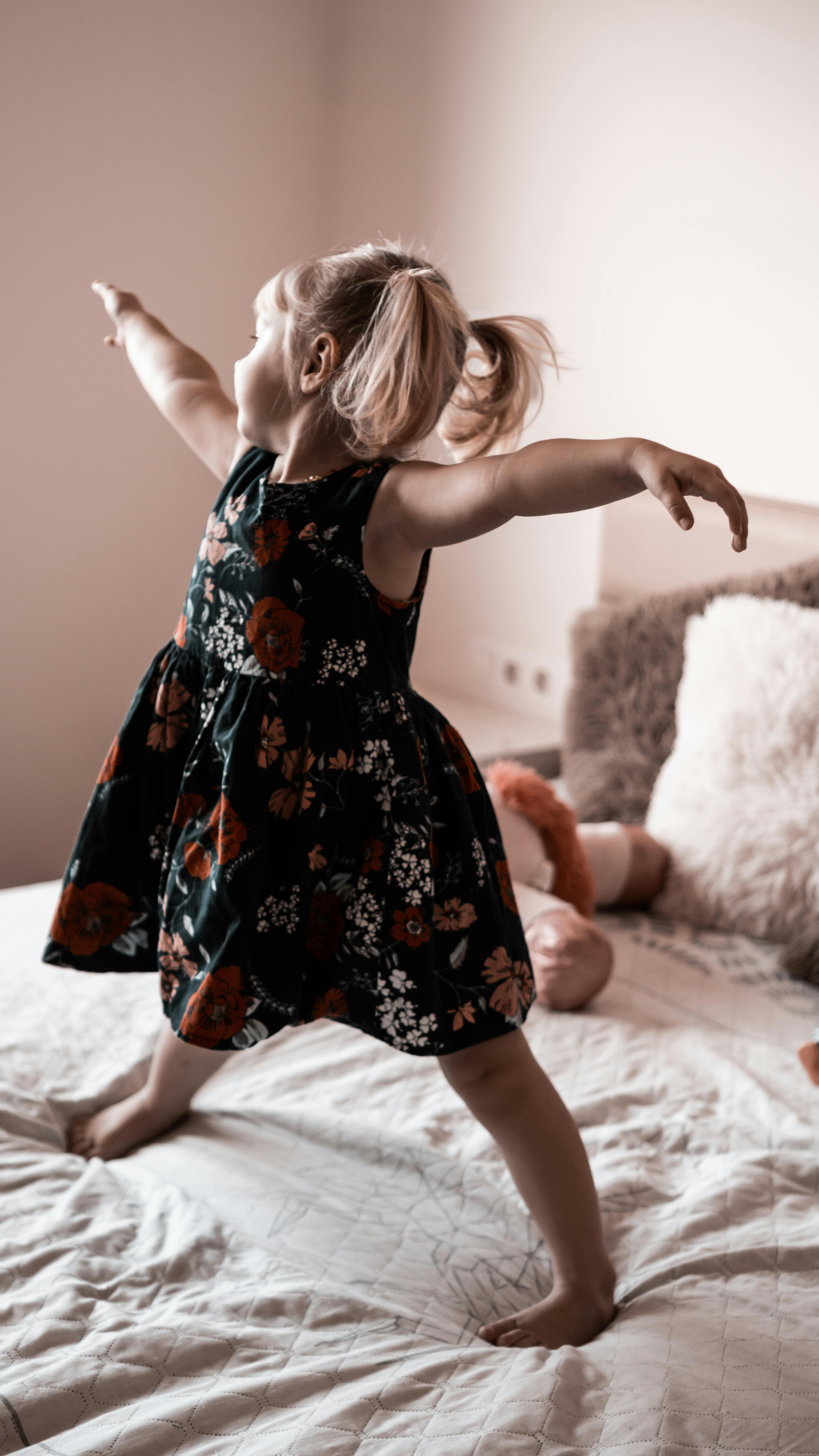 Cute little girl standing on bed in star pose · Free Stock Photo
