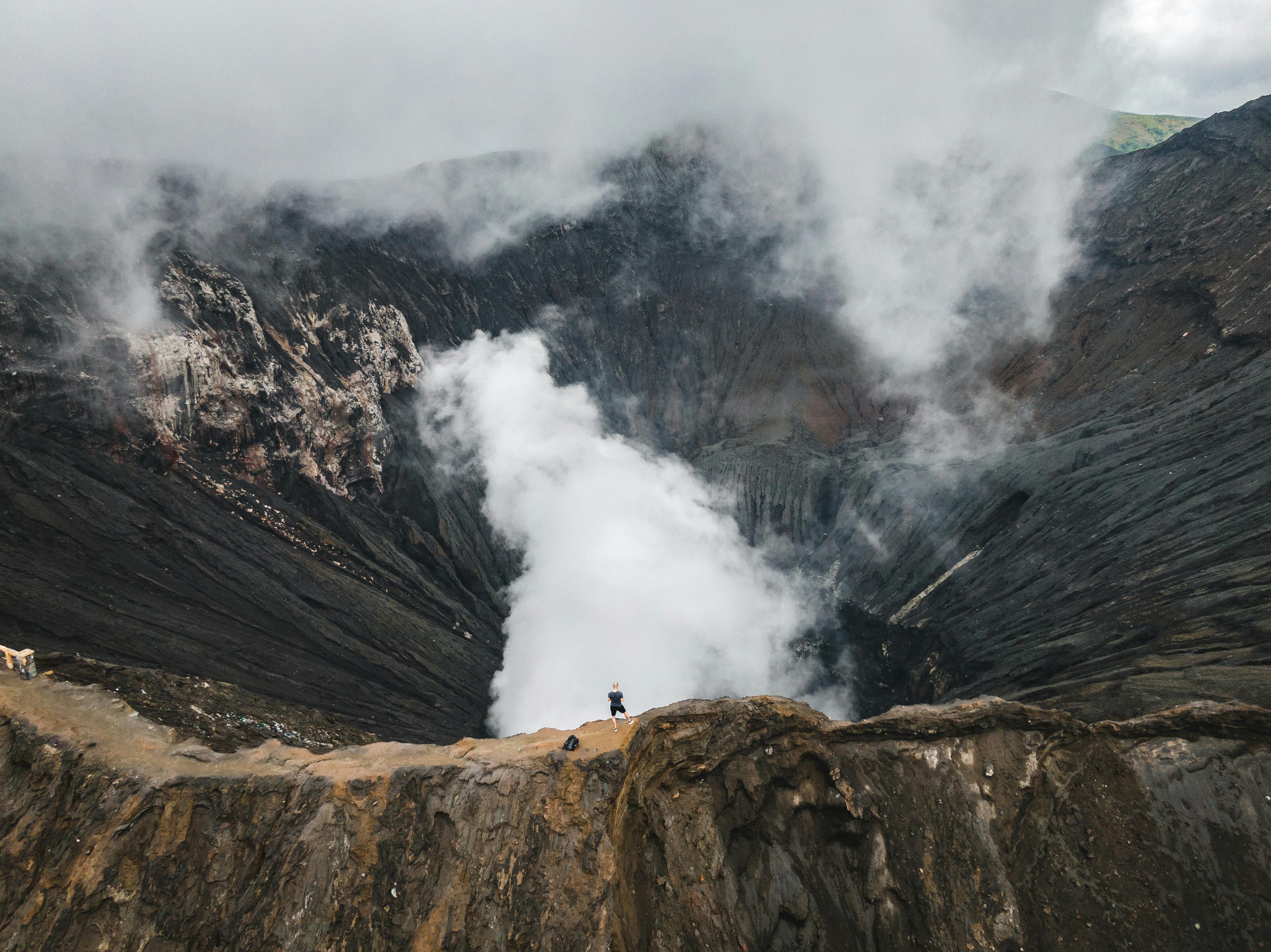 Person standing on edge of soaring volcano · Free Stock Photo