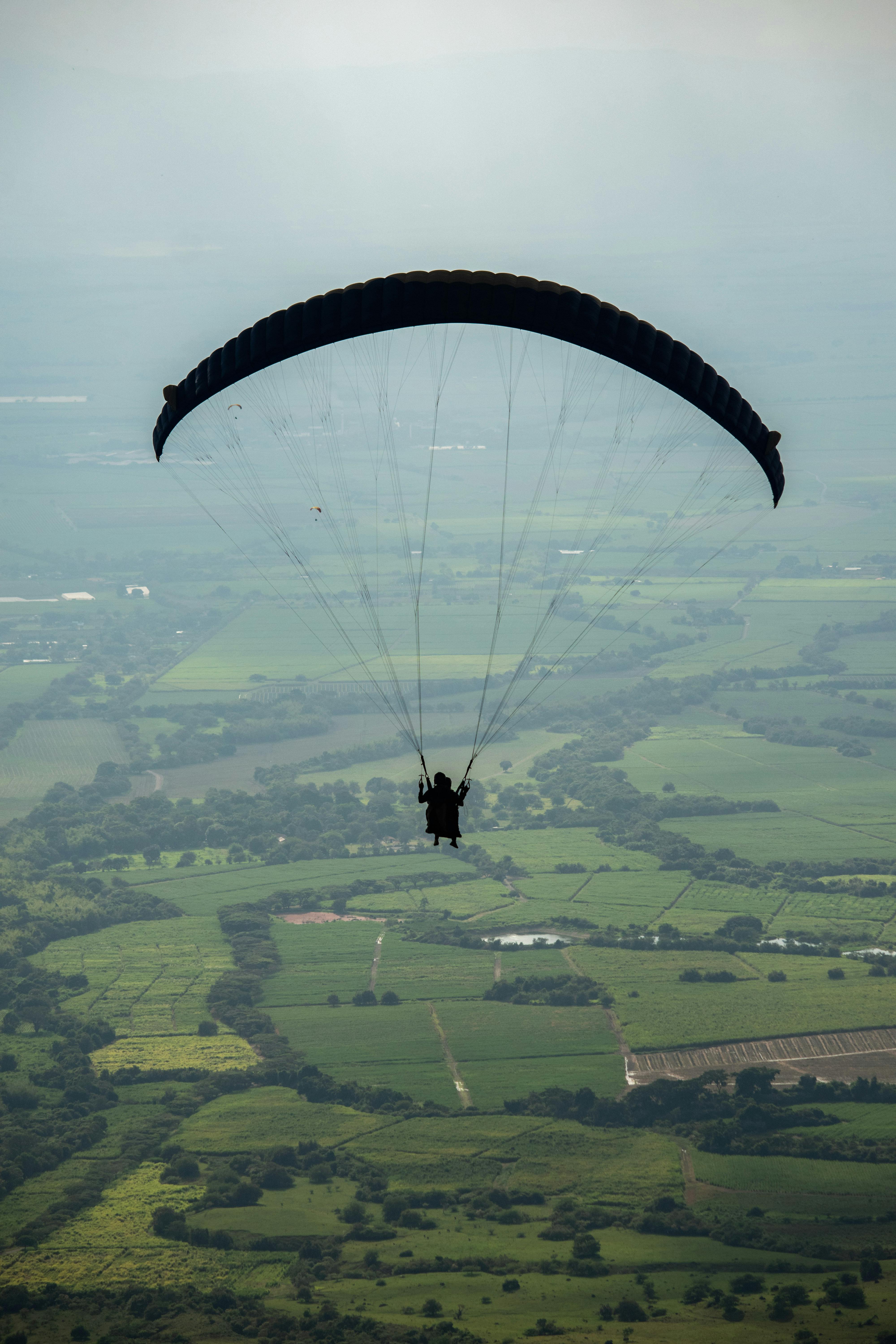 Faceless person flying paraglider over green countryside · Free Stock Photo