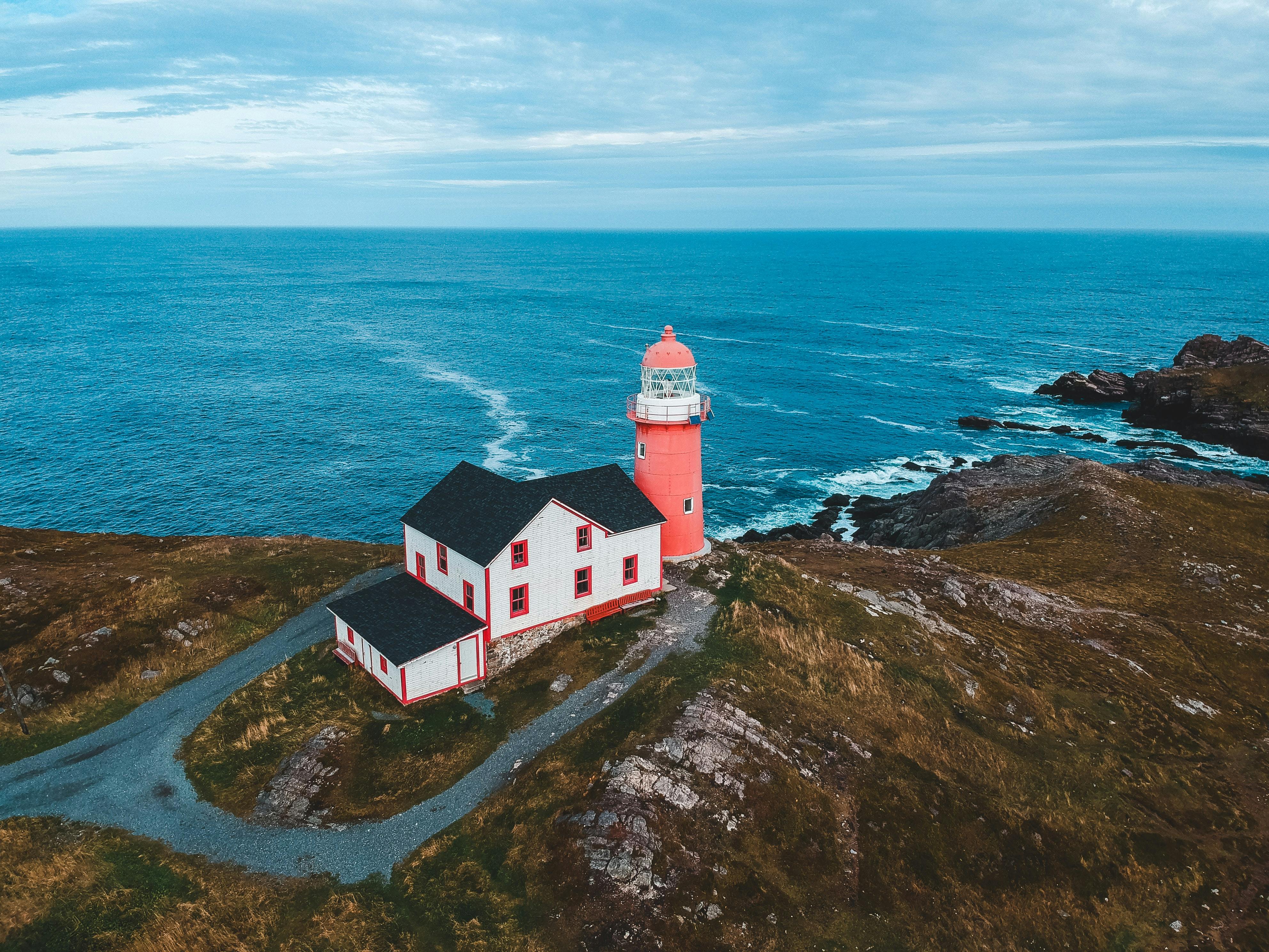 Bright ocean near lighthouse and building under blue sky · Free Stock Photo