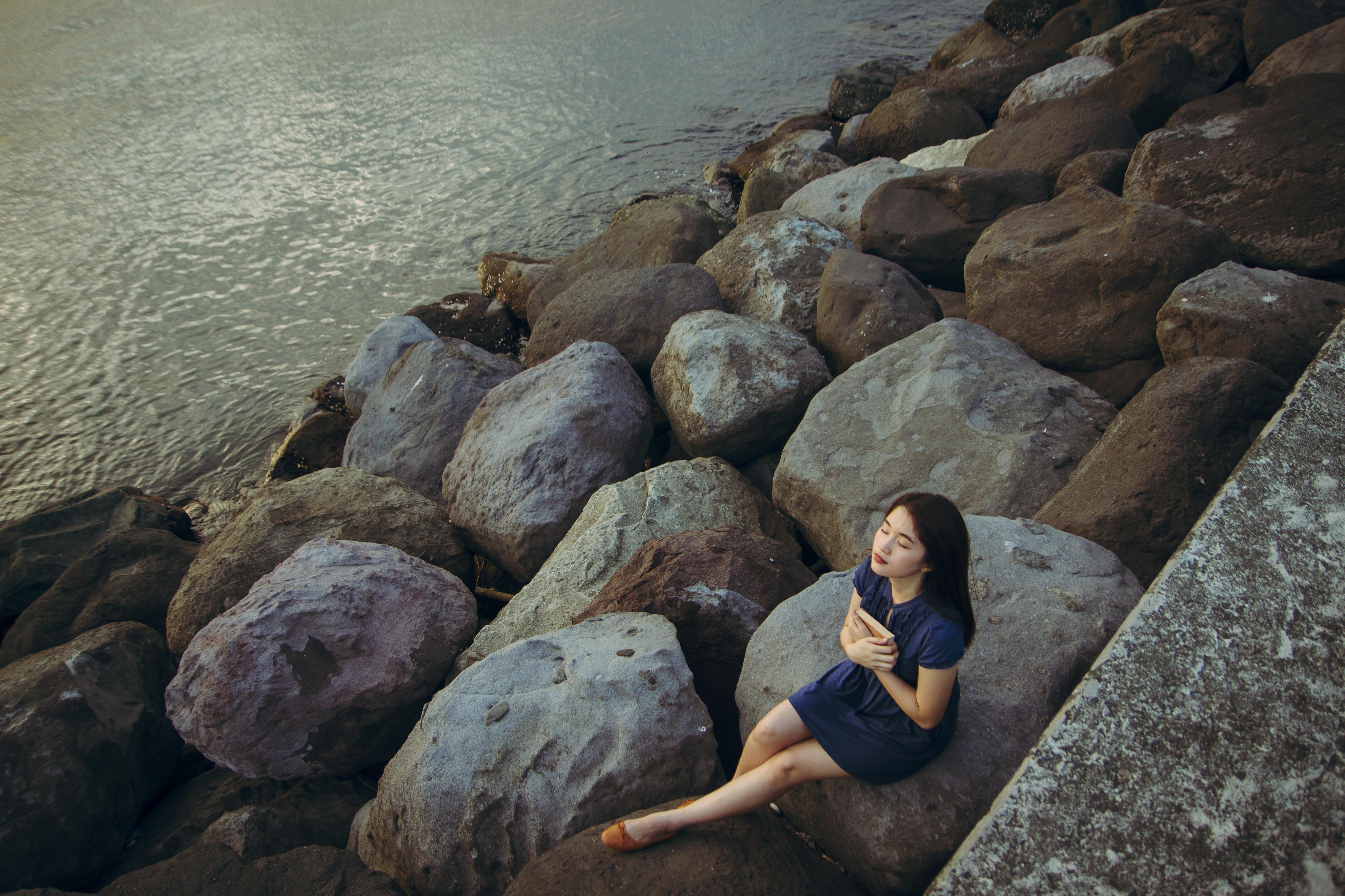 Woman in Blue Dress Sitting on Rock Near Body of Water · Free Stock Photo