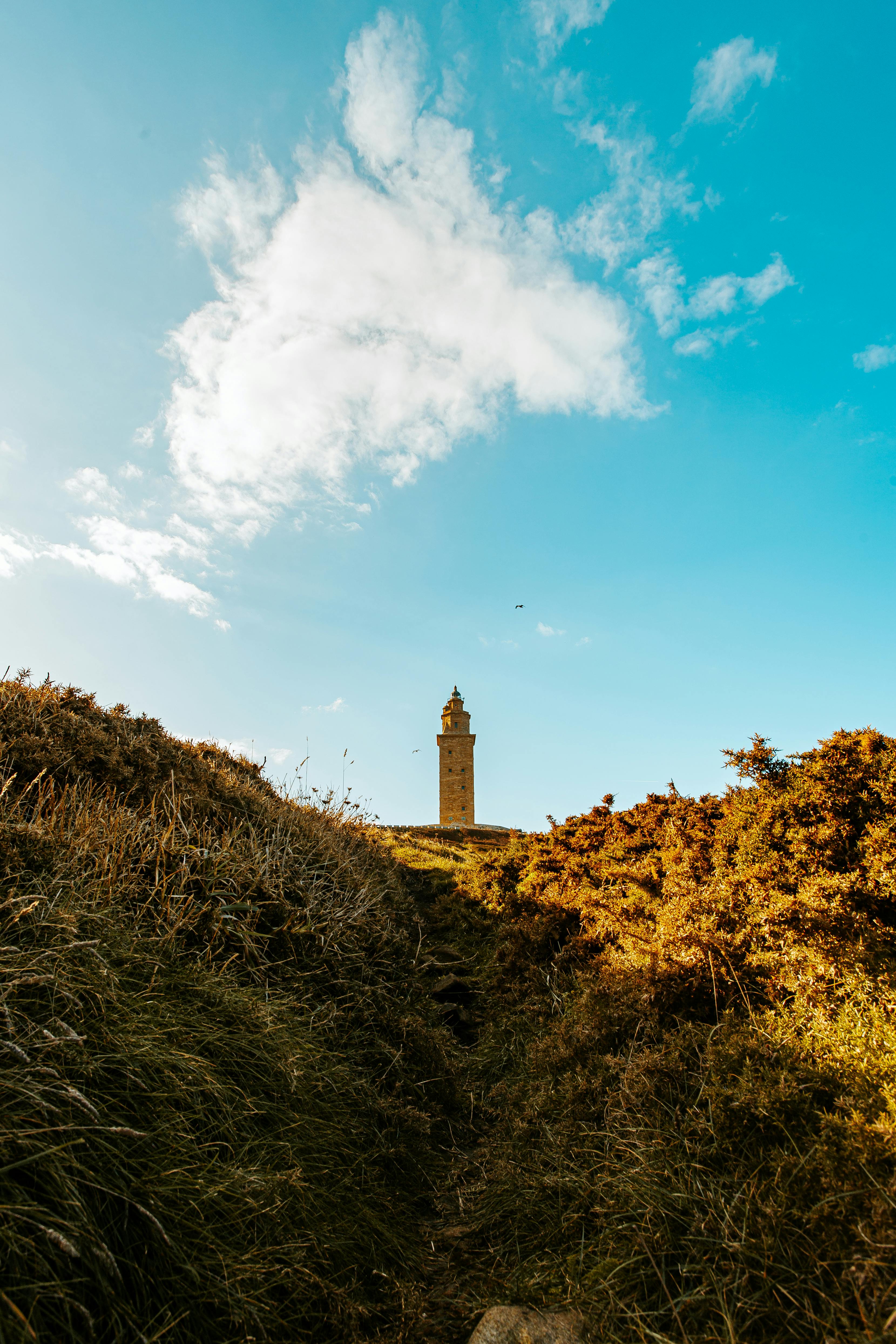 Old lighthouse on hill with faded grass under cloudy sky · Free Stock Photo