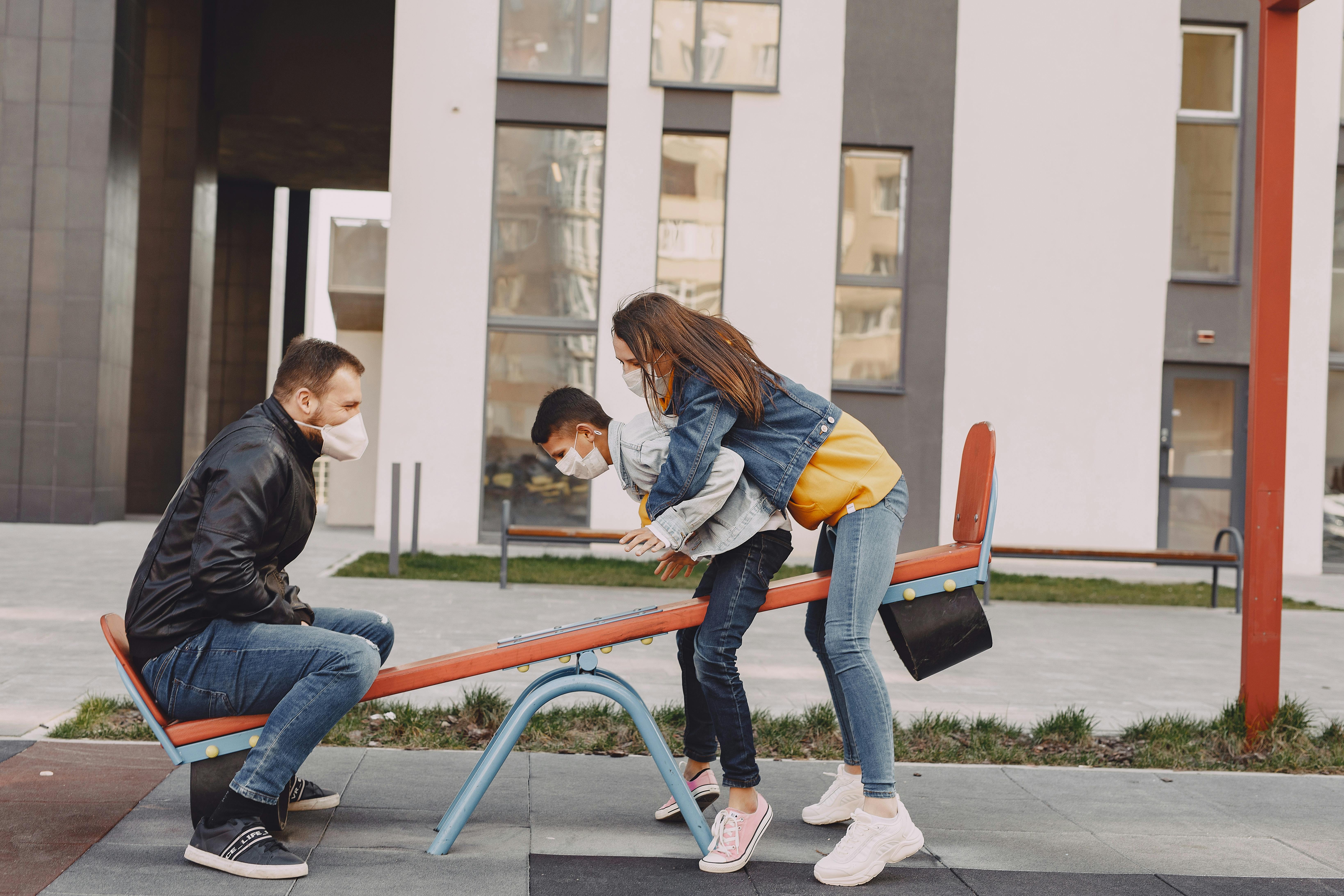 Family in mask swinging on seesaw on playground · Free Stock Photo