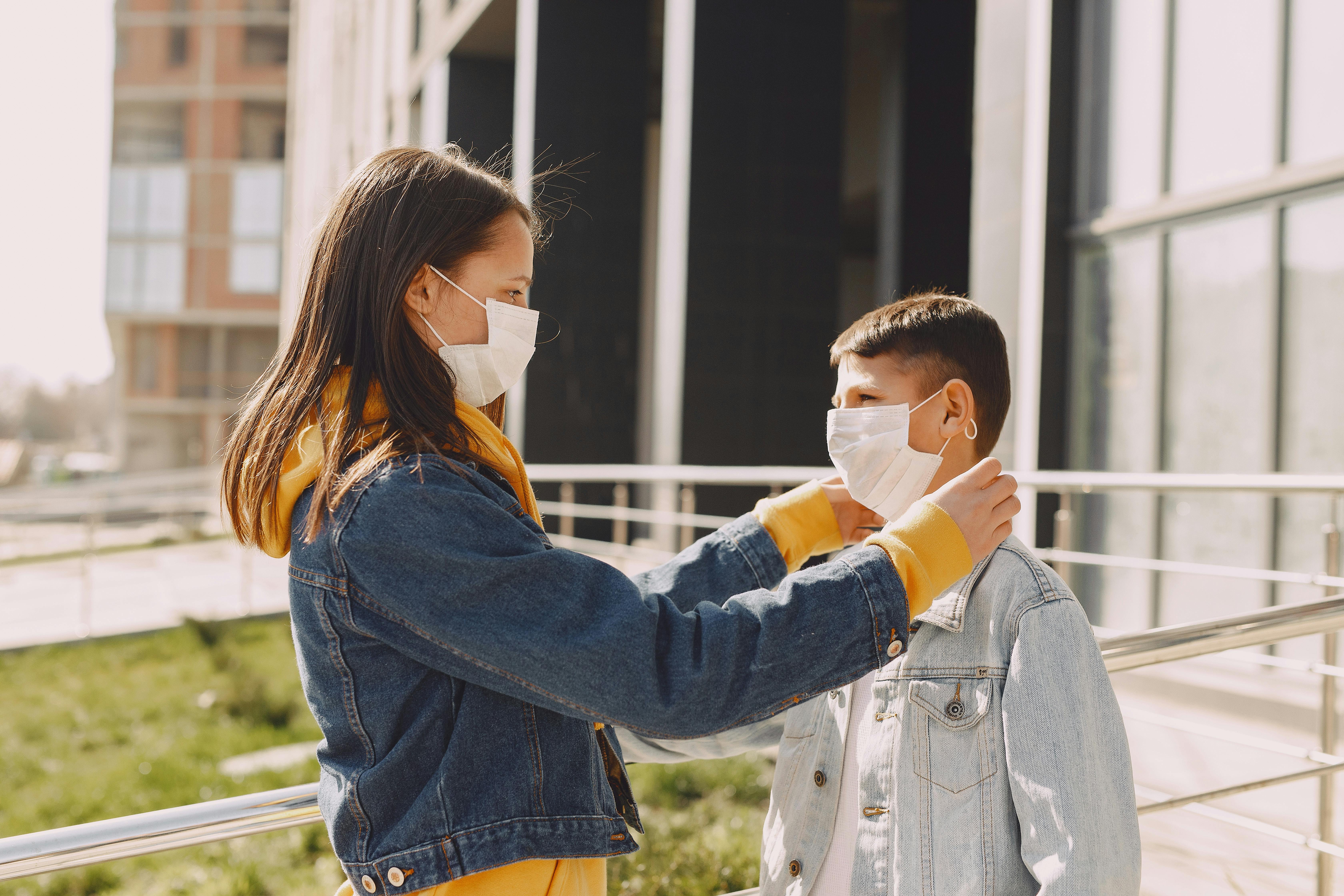 Girl in medical mask fixing medical mask on boy face · Free Stock Photo