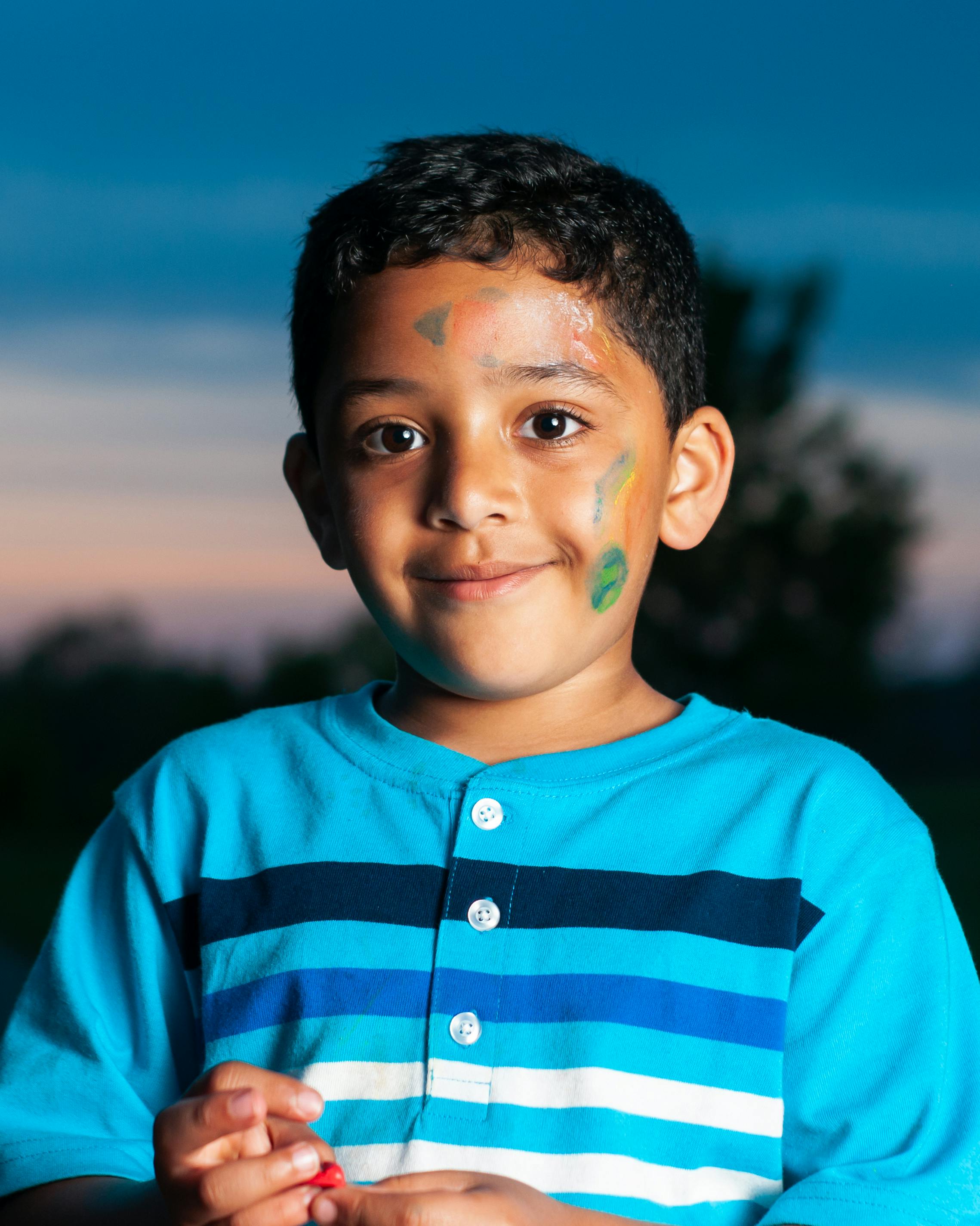 Smiling ethnic boy in bright wear near trees at sunset · Free Stock Photo