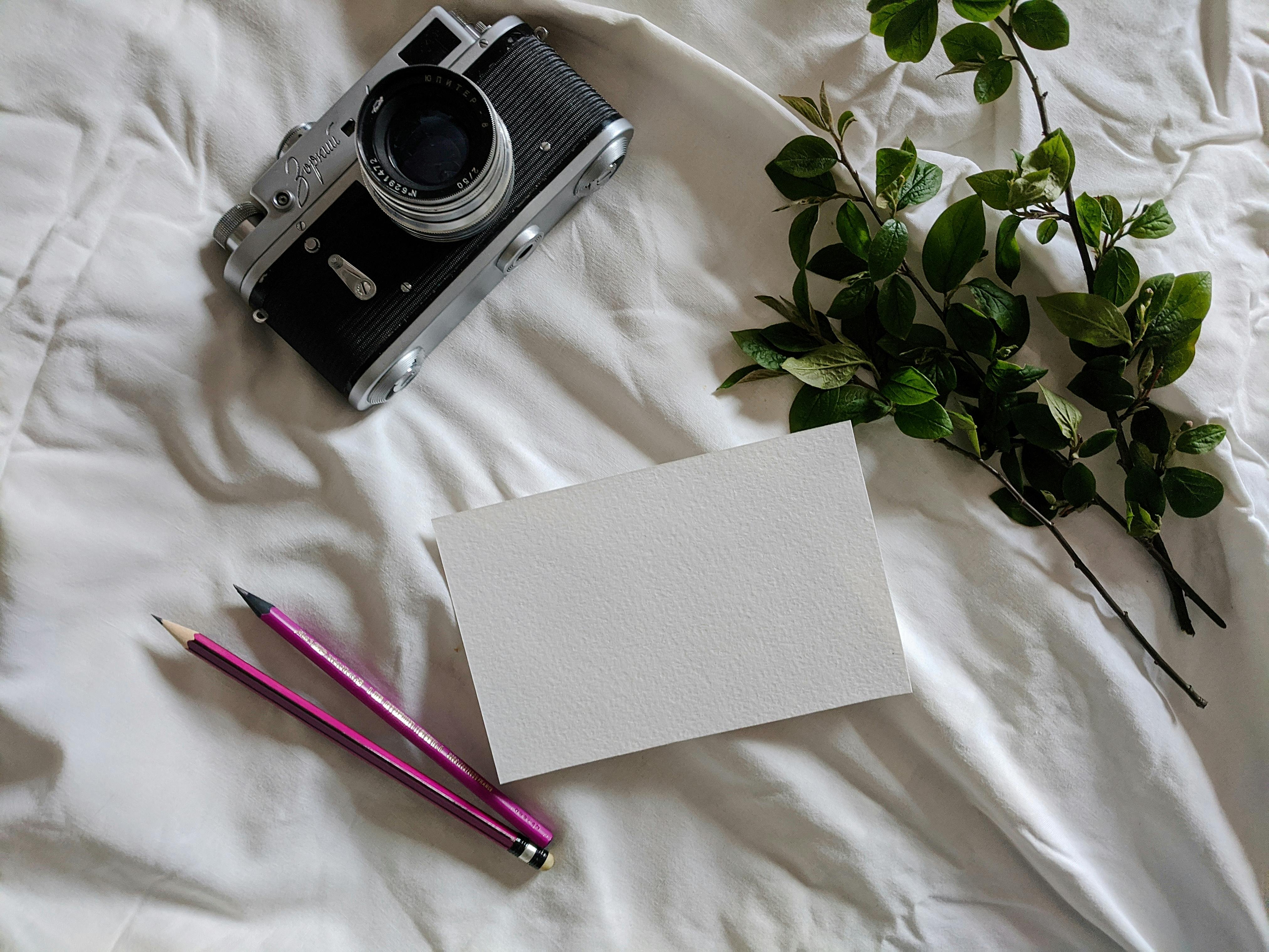Close-Up Shot of Camera and Paper on a White Textile · Free Stock Photo