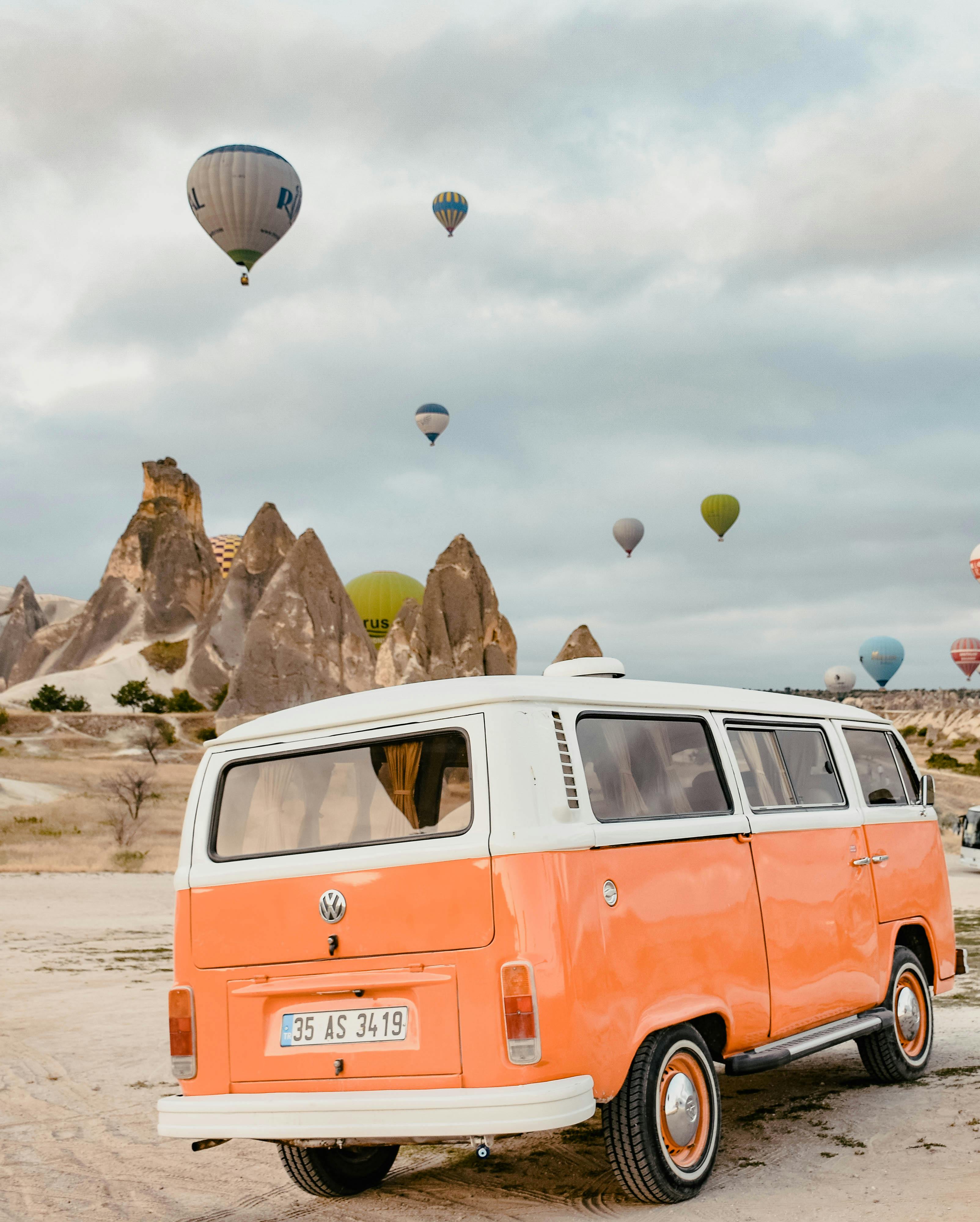 Multicolored air balloons flying over cliffs and parked retro van ...