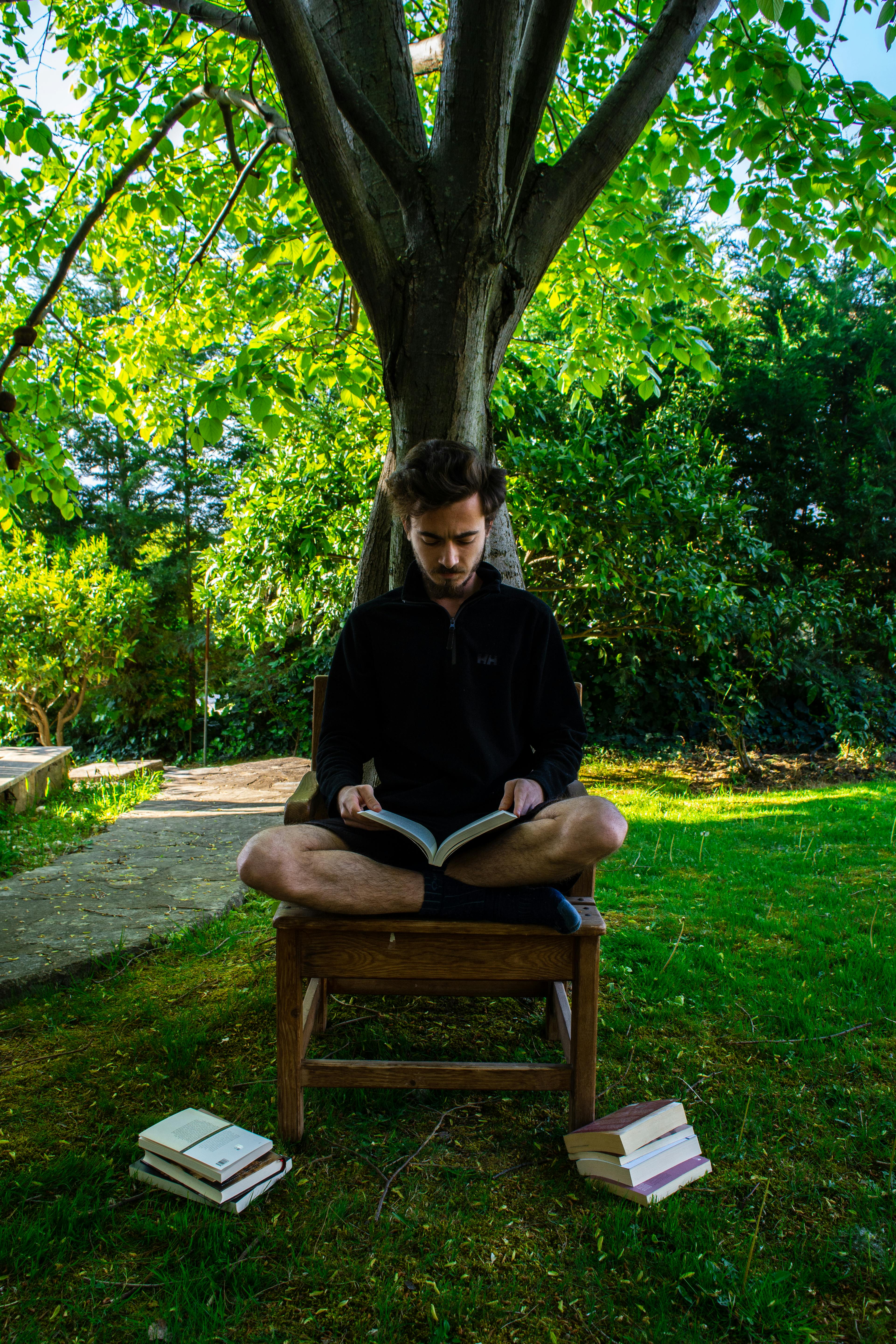 A Man Sitting on Wooden Chair while Reading a Book · Free Stock Photo