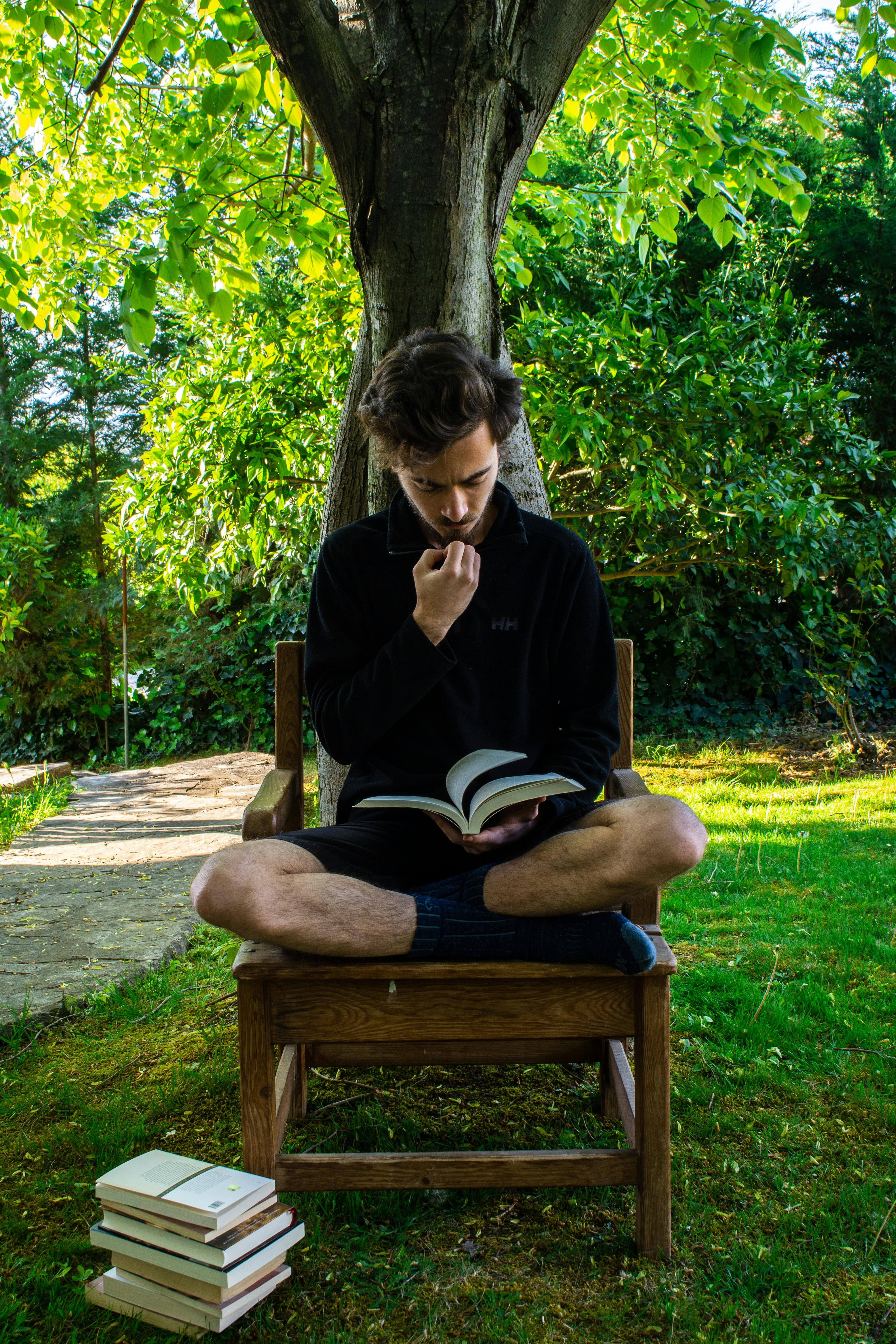 A Man Sitting on Wooden Chair while Reading a Book · Free Stock Photo