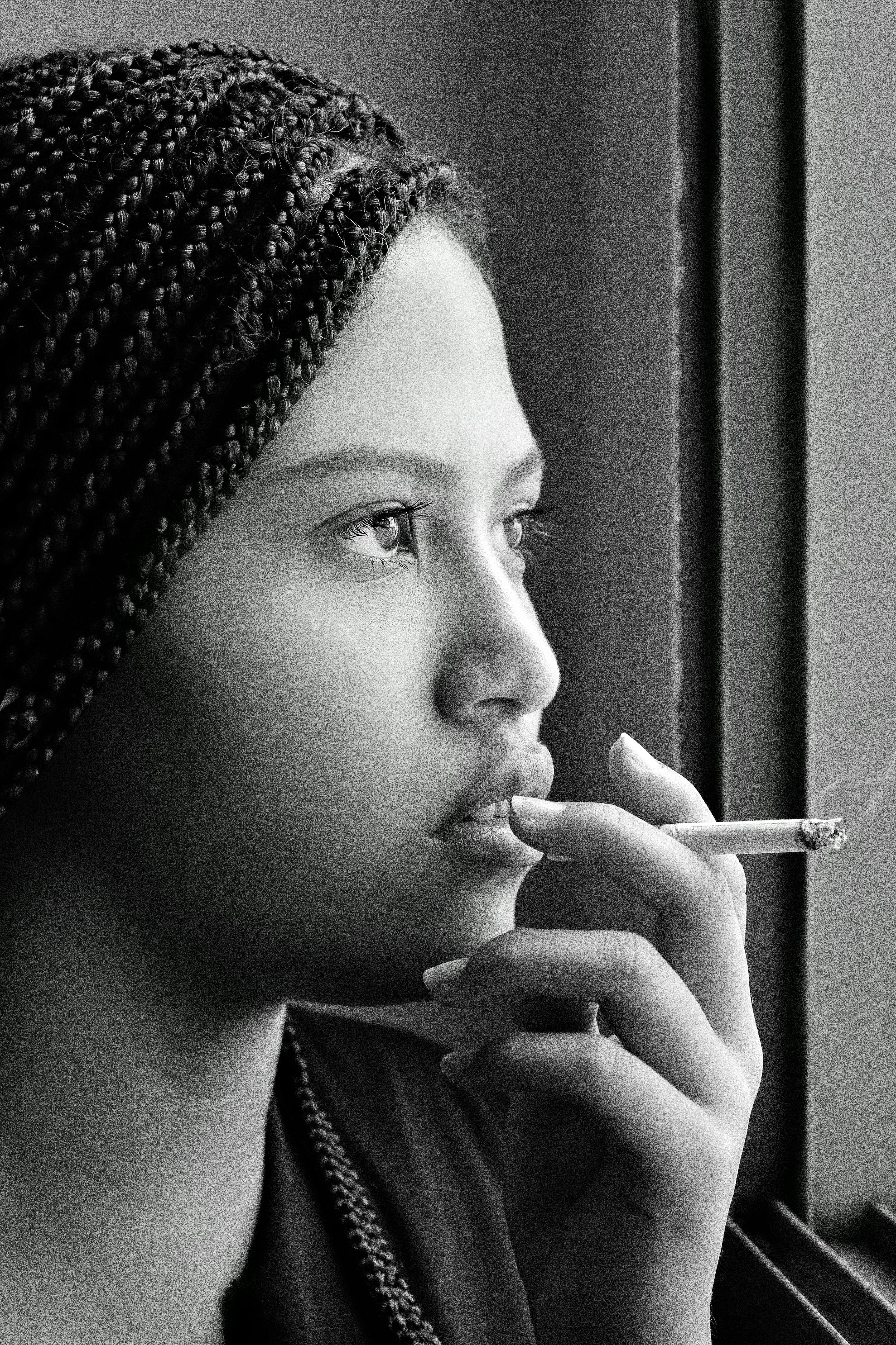 Crop pondering black woman smoking cigarette near window at home · Free ...
