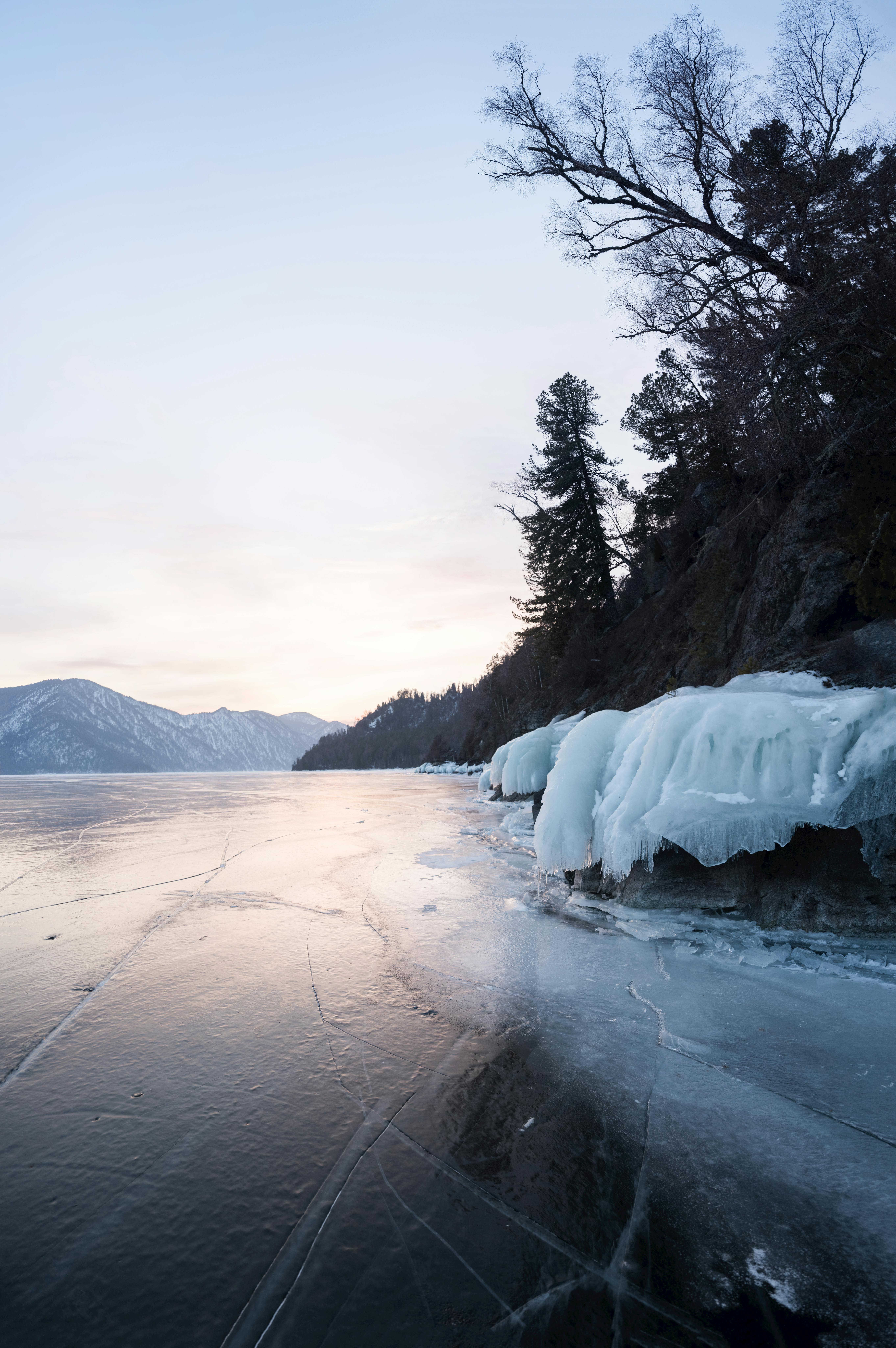 Frozen lake surrounded by mountains and trees in winter · Free Stock Photo