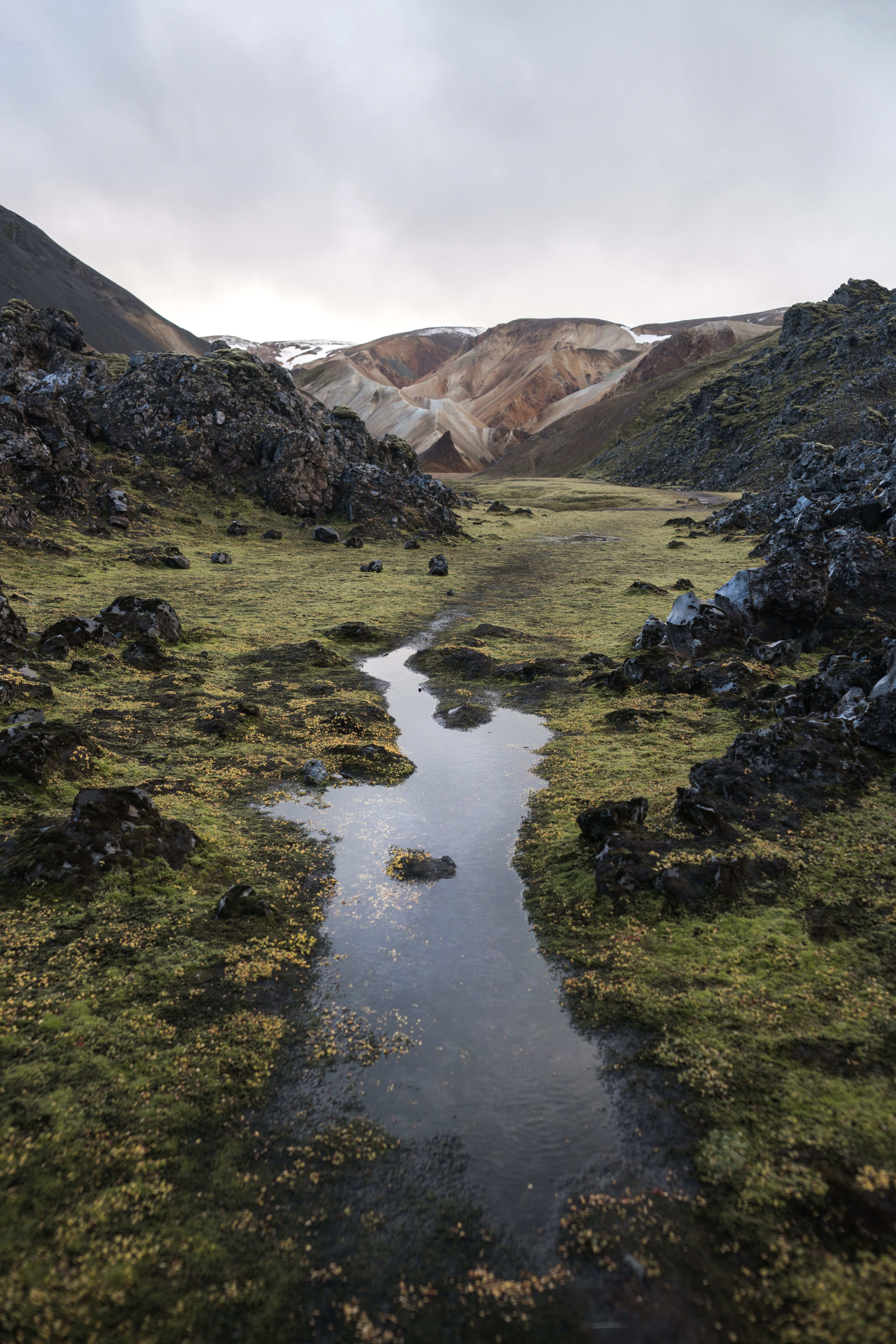 Narrow river in mountainous terrain under cloudy sky · Free Stock Photo