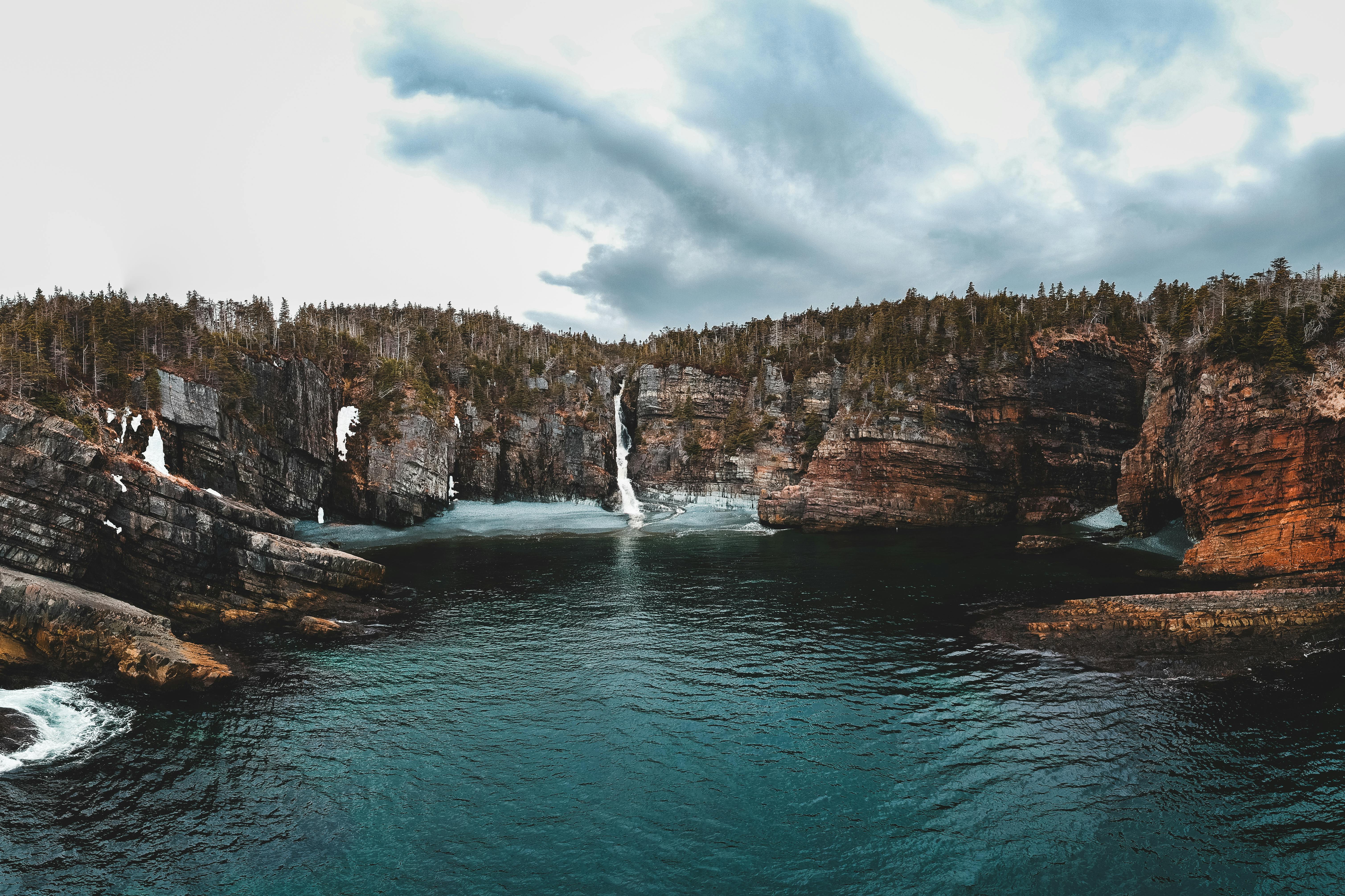 Rocky ravine with waterfall flowing into blue sea · Free Stock Photo