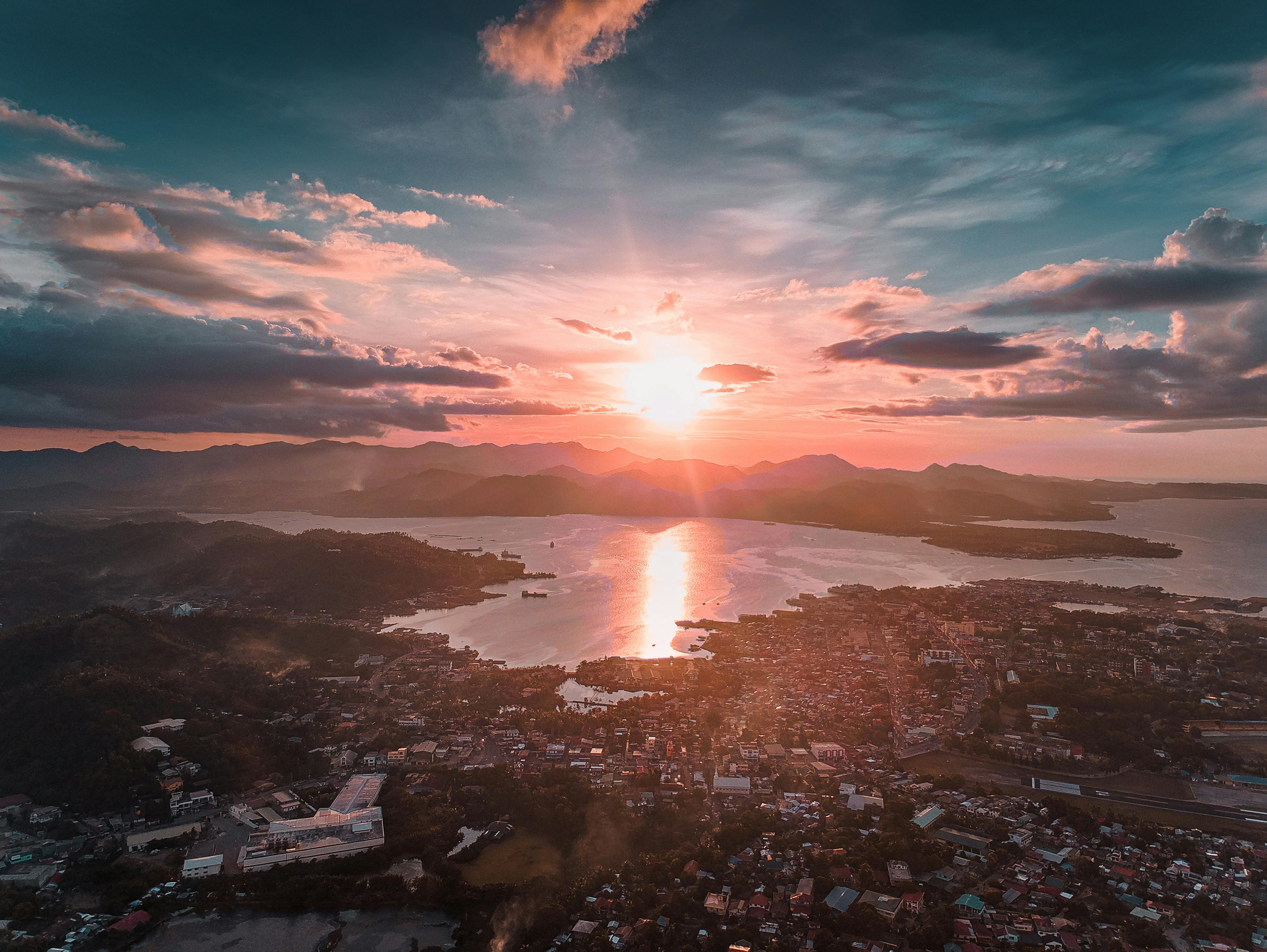 Bright sun over sea and coastal city during sundown · Free Stock Photo