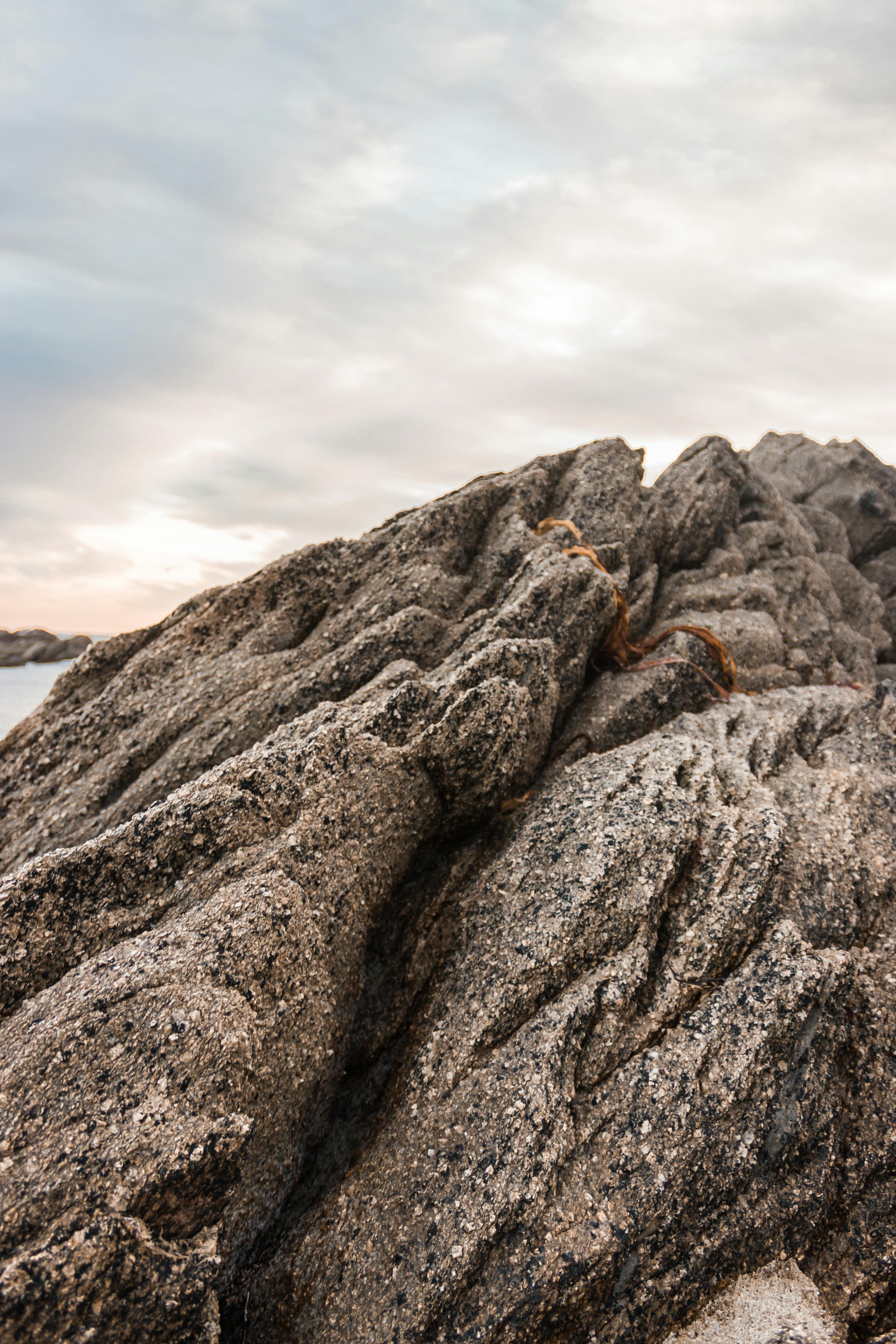Rough rock under cloudy sky in evening · Free Stock Photo