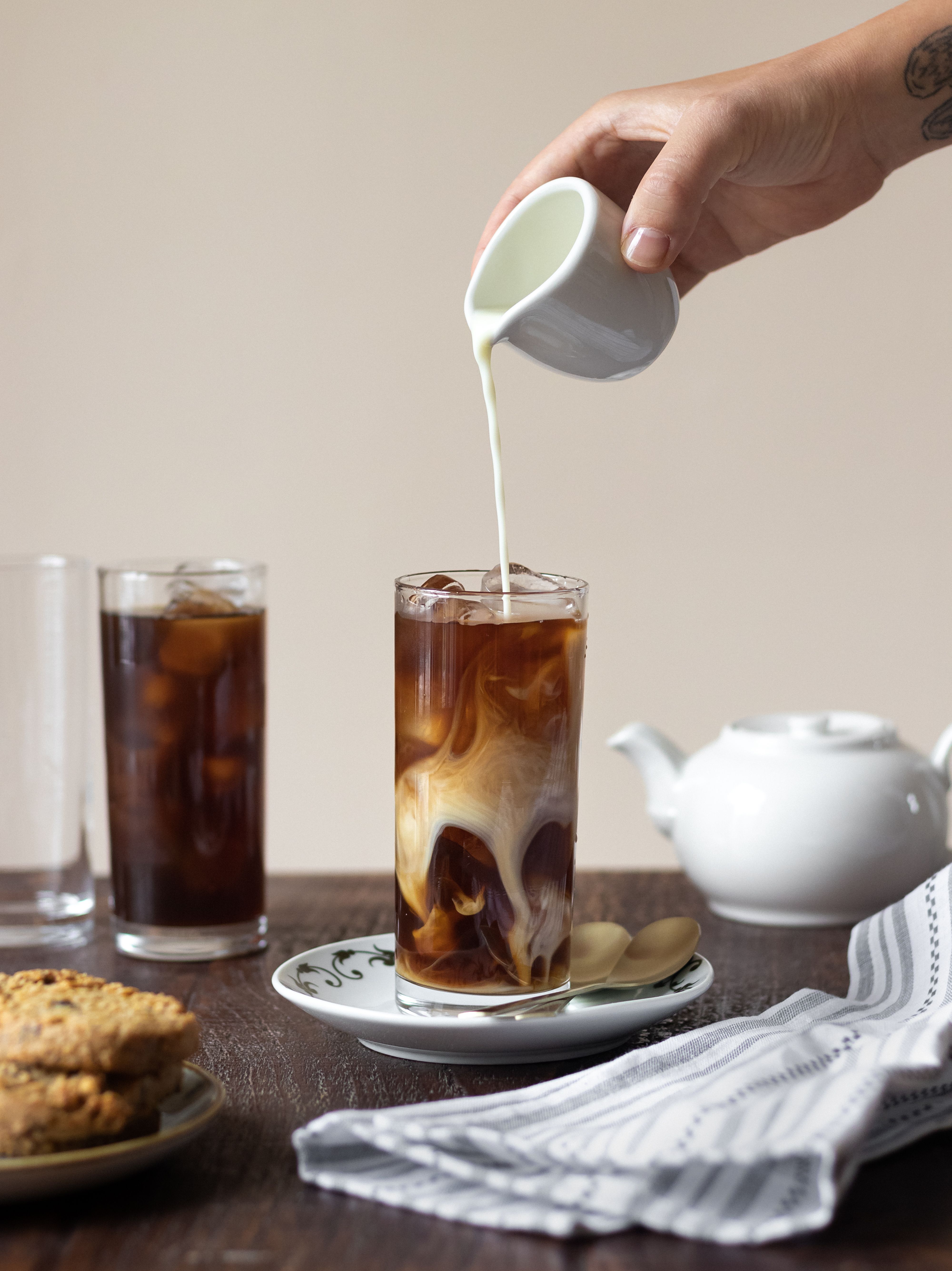 Crop person pouring cream into iced coffee for breakfast · Free Stock Photo