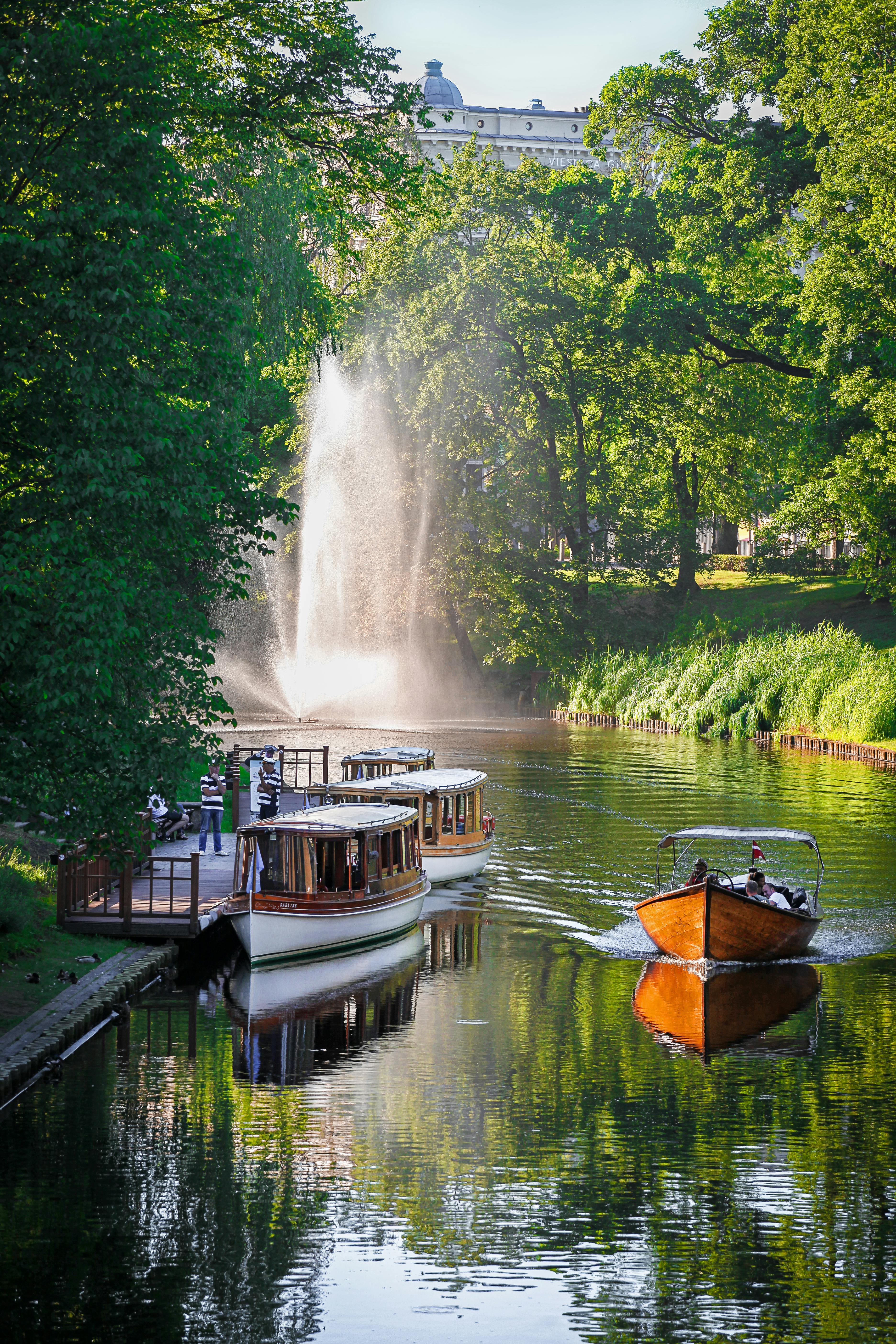 Lake with floating boats behind cascade near lush green trees · Free ...