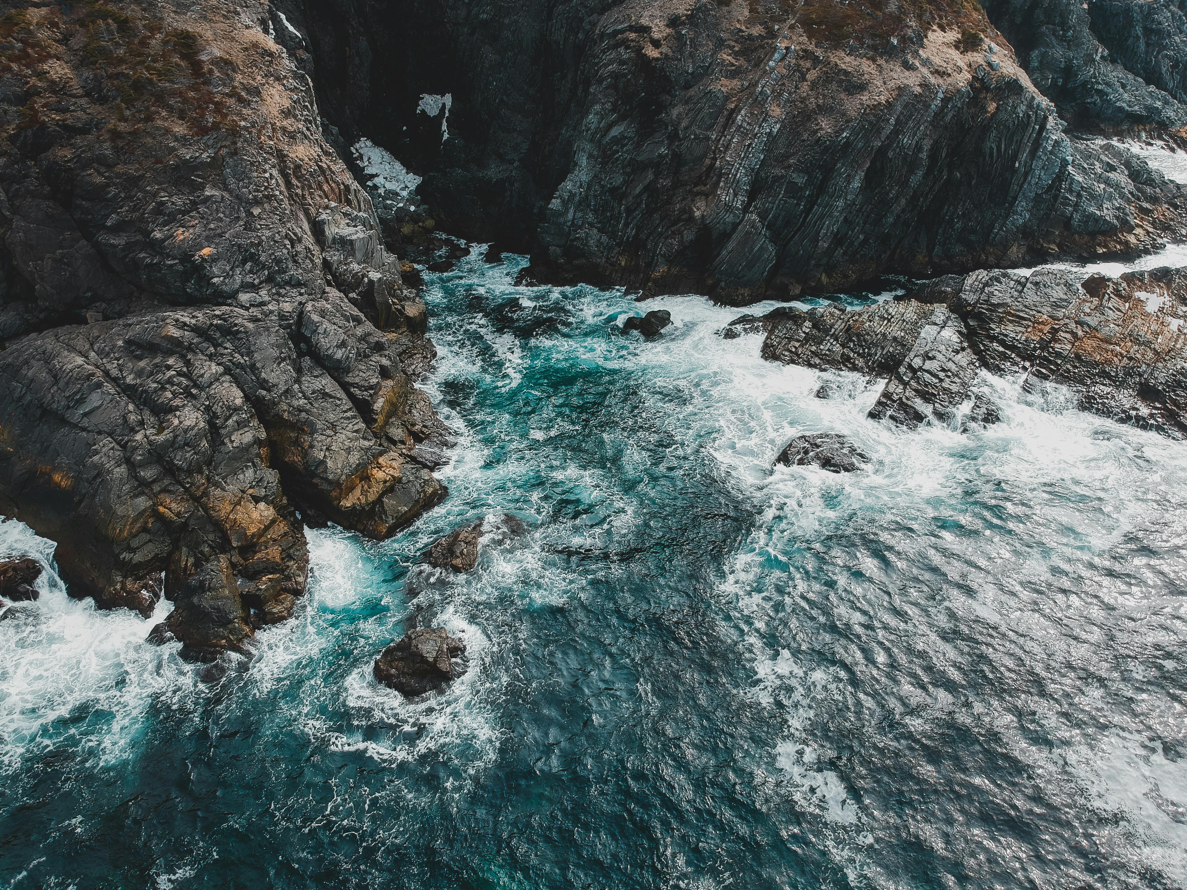 Rocky cliff near waving clear sea · Free Stock Photo