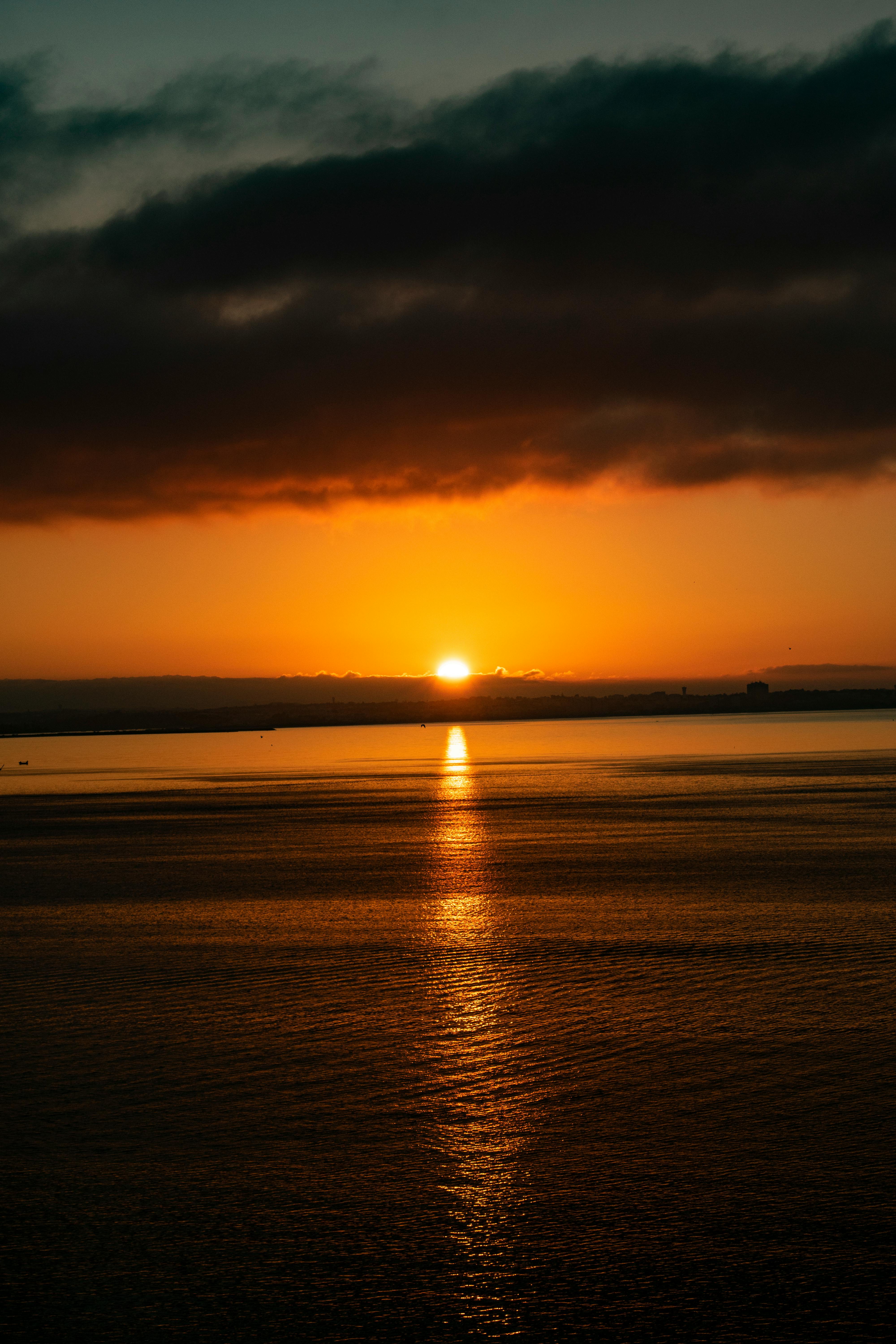 Sea near mountains under bright sky at sunset at night · Free Stock Photo