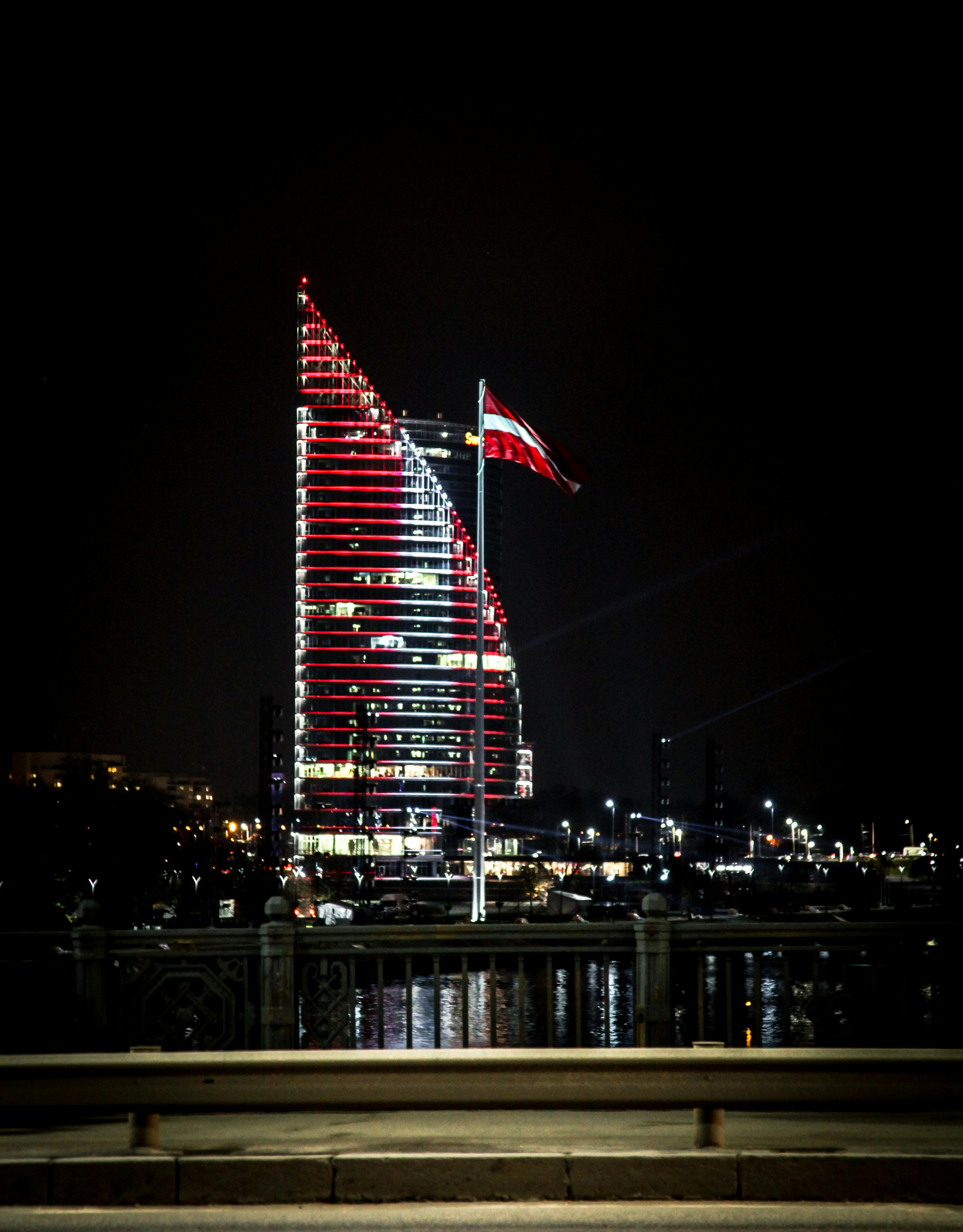 Illuminated modern glass tower on riverside at night · Free Stock Photo