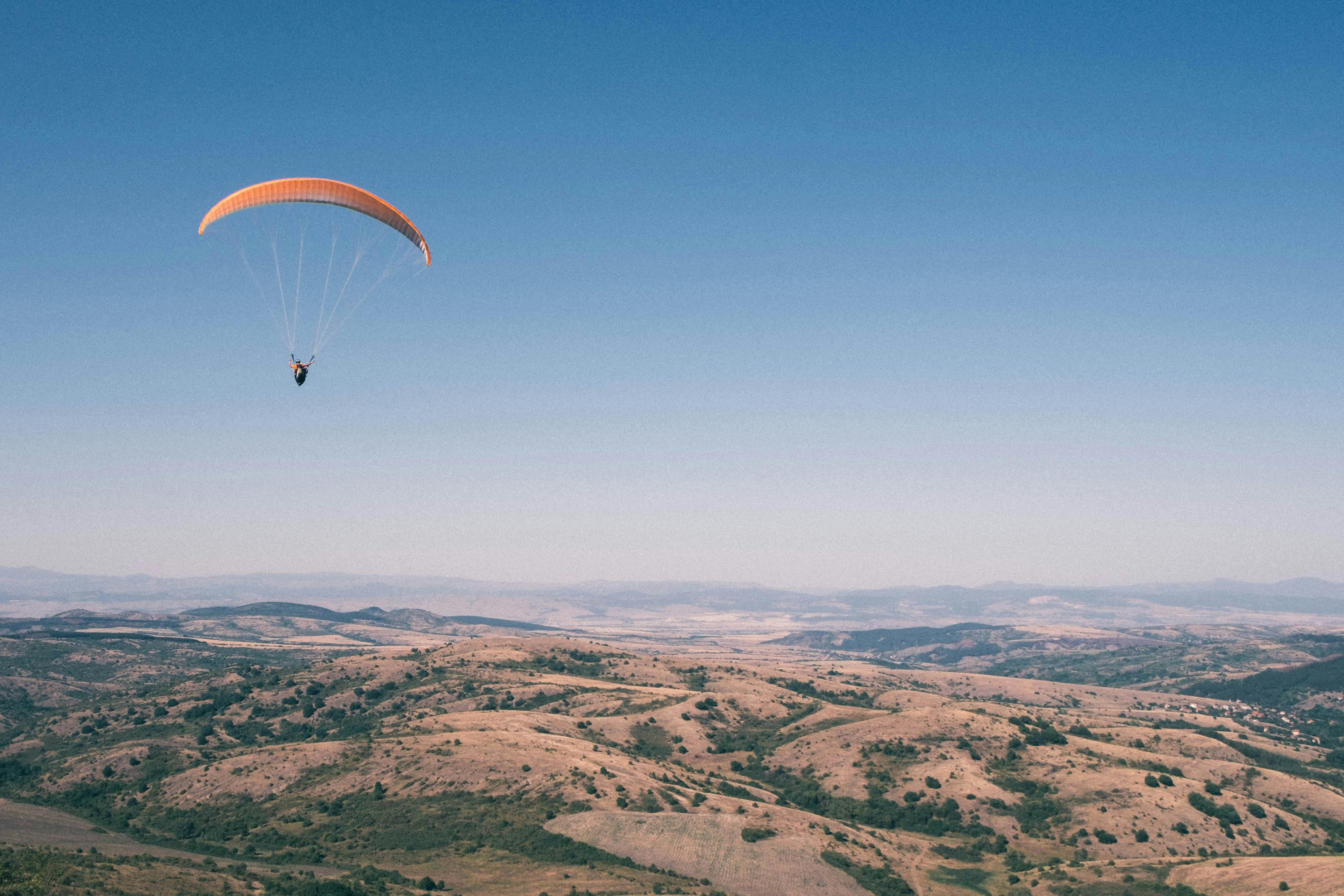 Aerial View of a Person Parachuting over Hills · Free Stock Photo