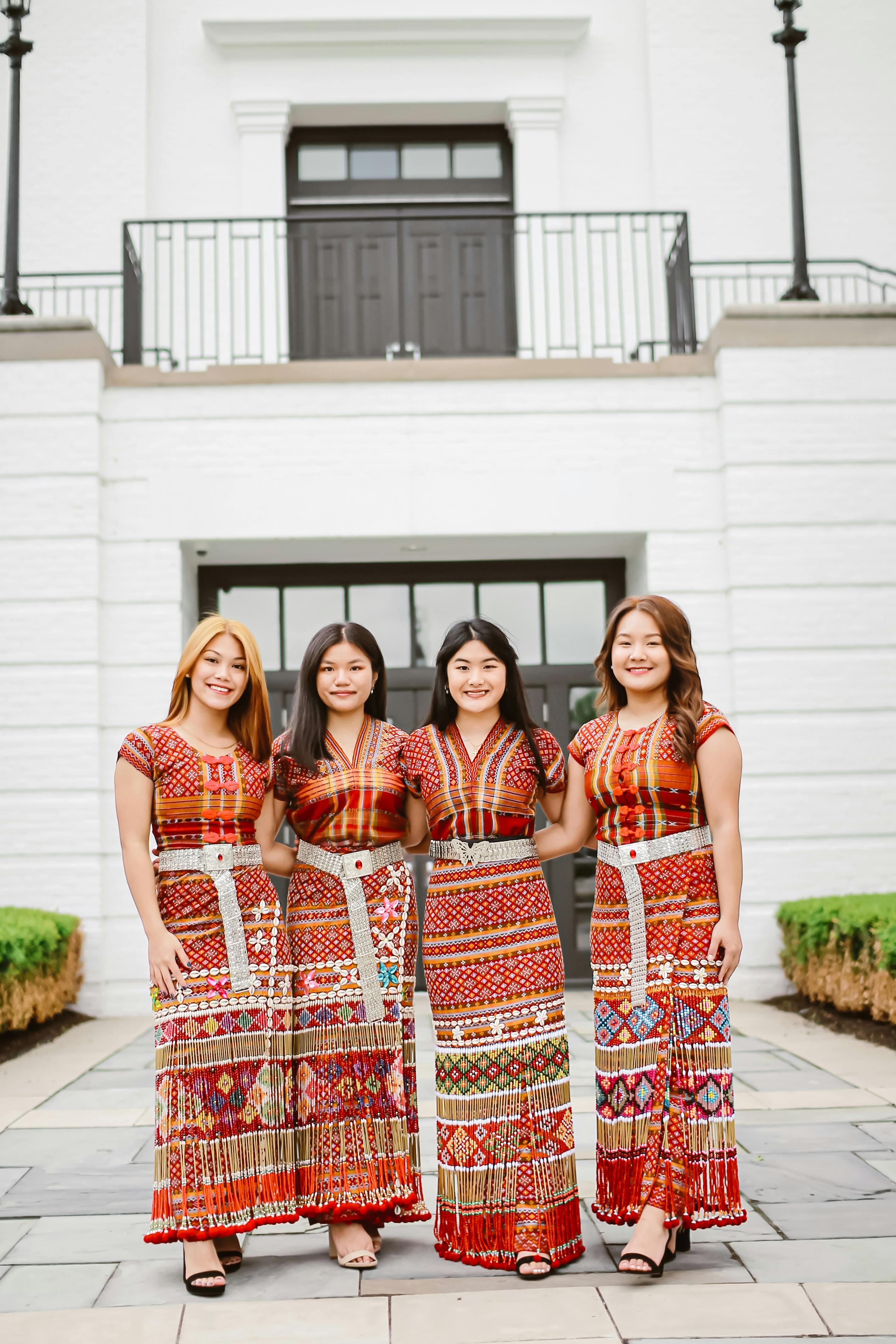 Cheerful Asian women in authentic dresses outside modern building ...