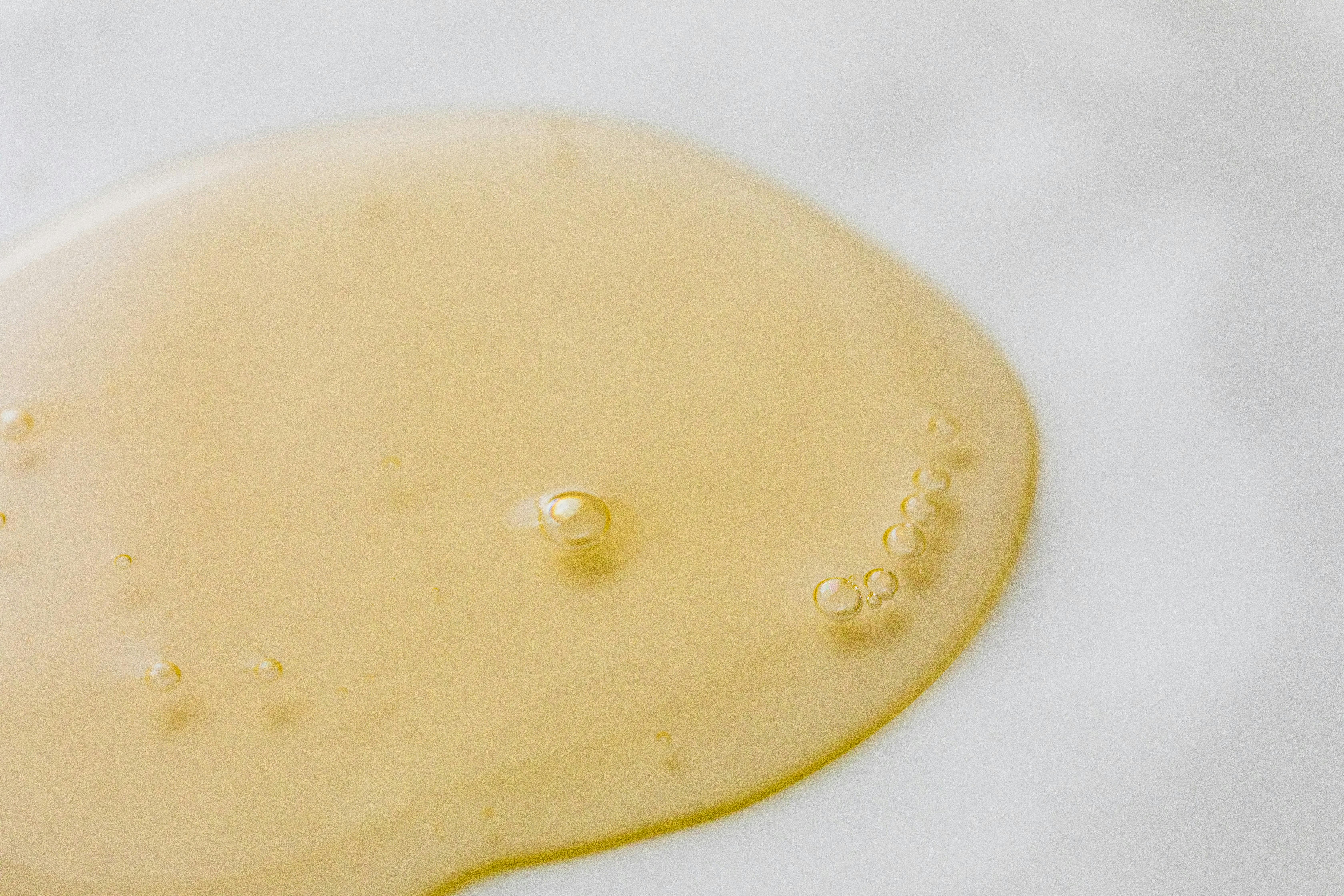 Transparent yellowish liquid on white surface · Free Stock Photo