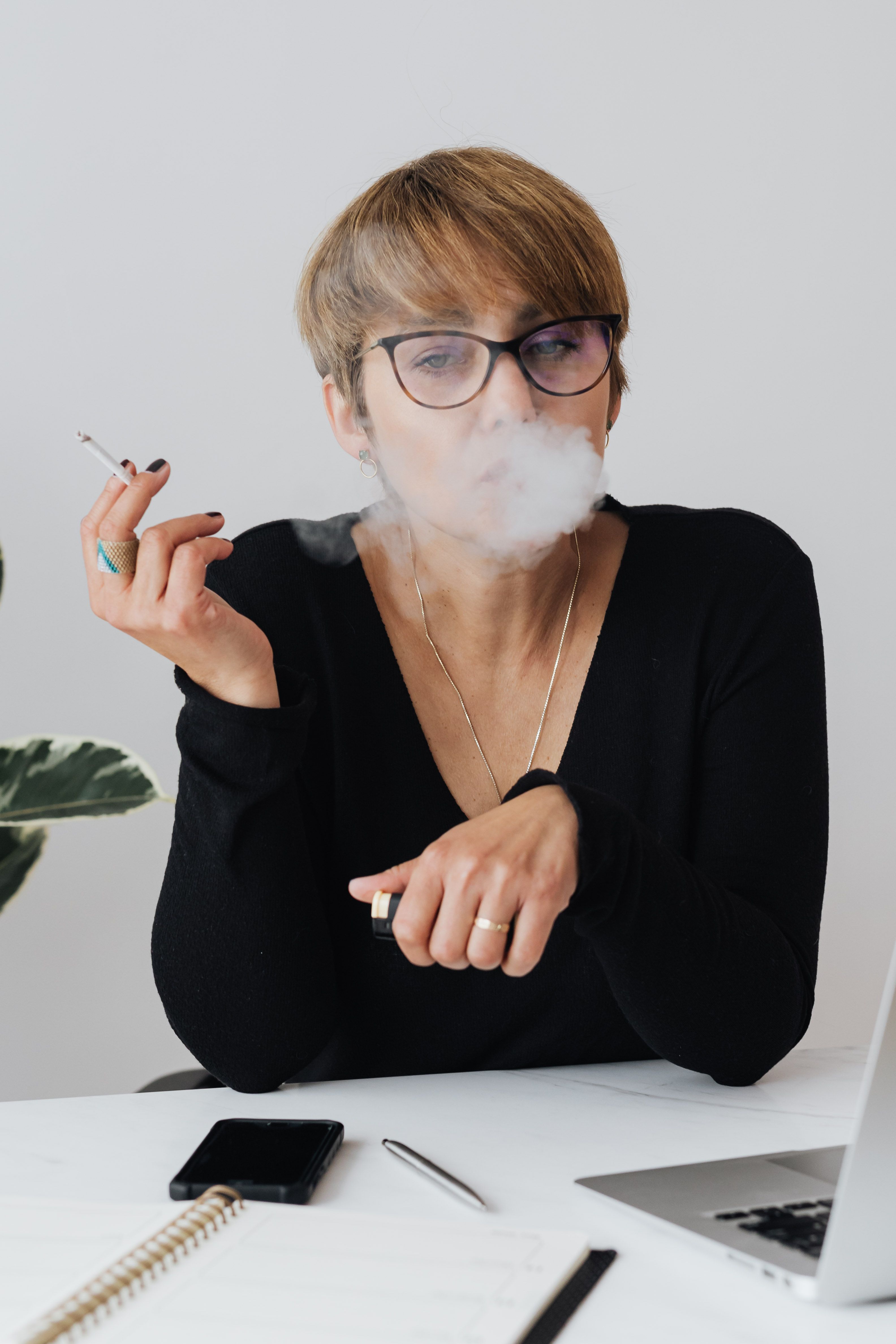 Thoughtful businesswoman smoking cigarette while sitting at table ...