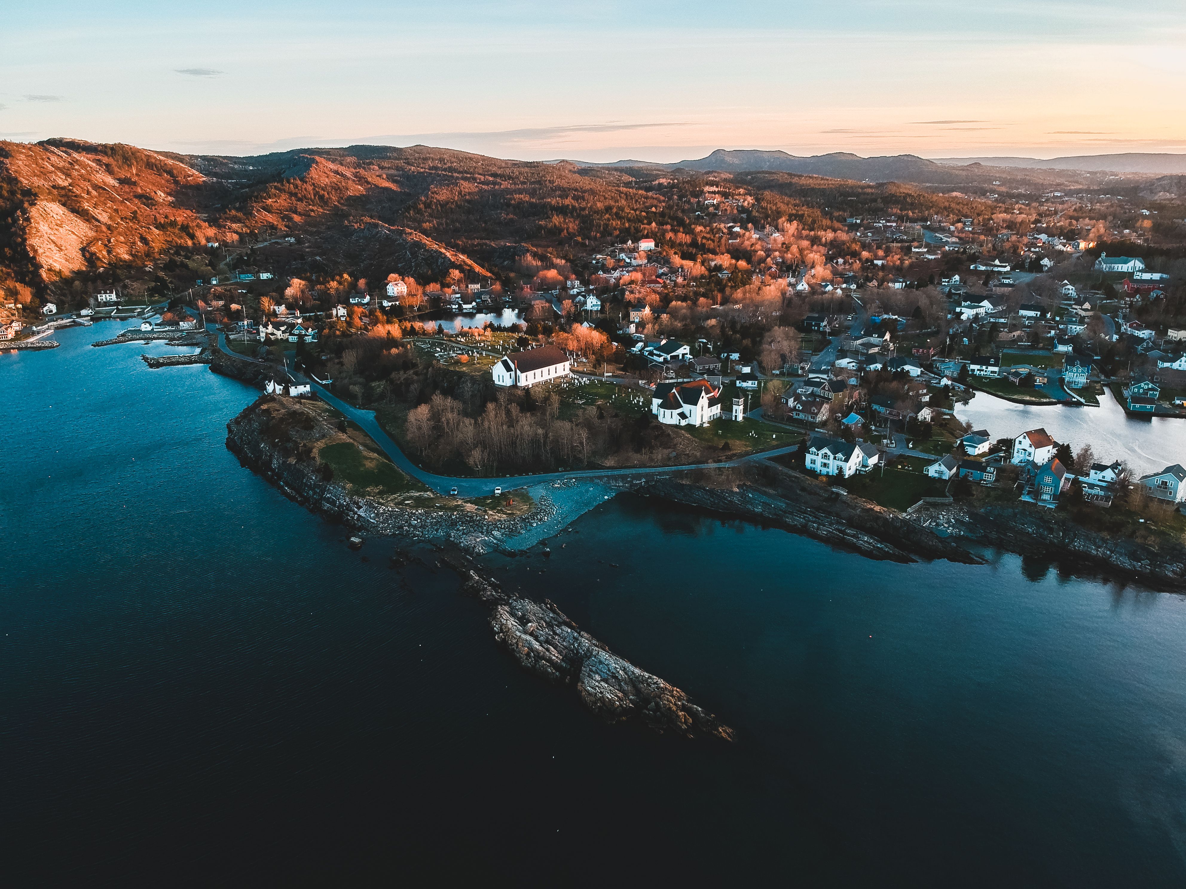 Ocean near ridge and dwelling houses at sunset · Free Stock Photo