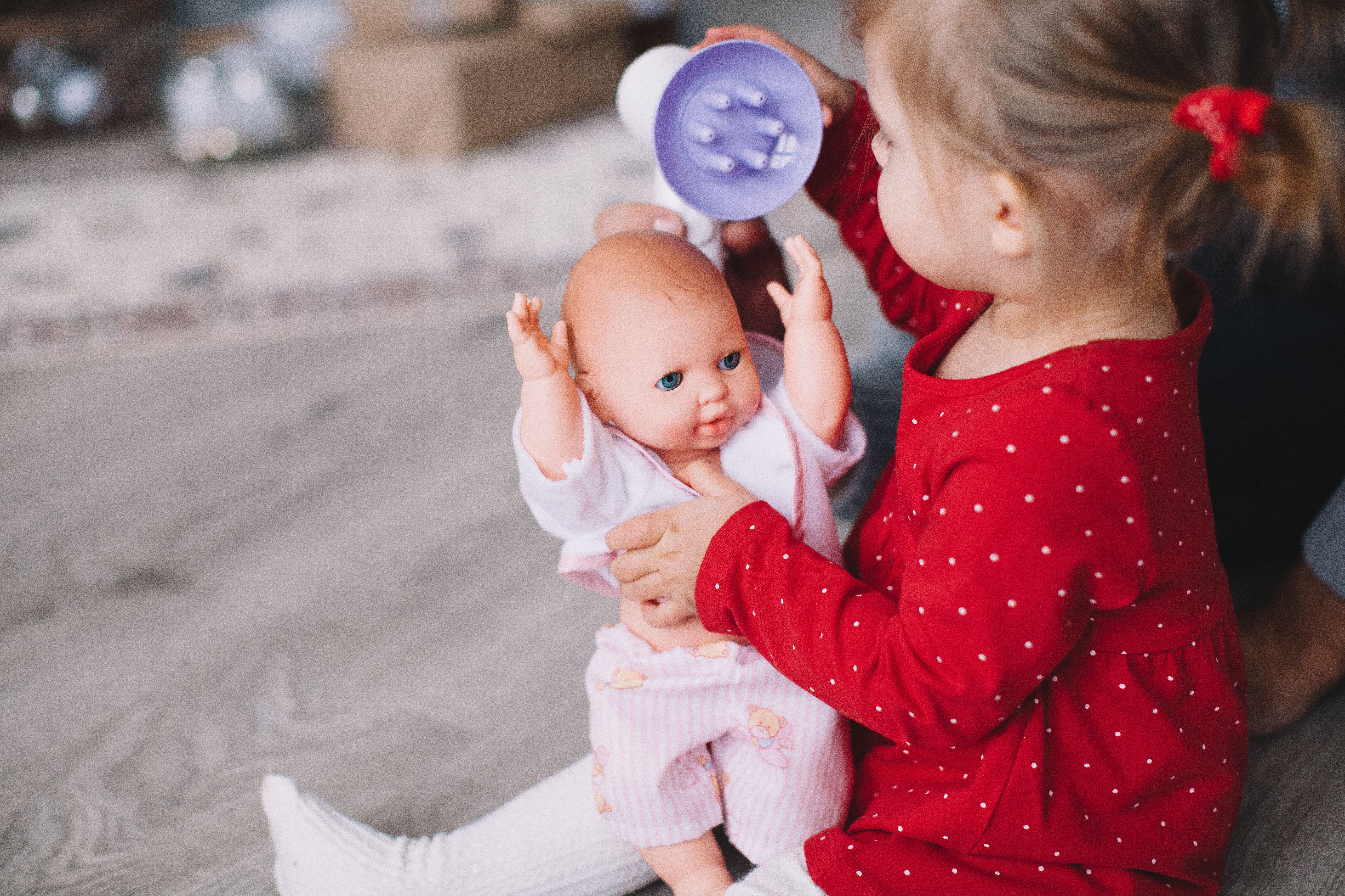 A Girl in Red Long Sleeve Dress Holding a Baby Doll Toy · Free Stock Photo