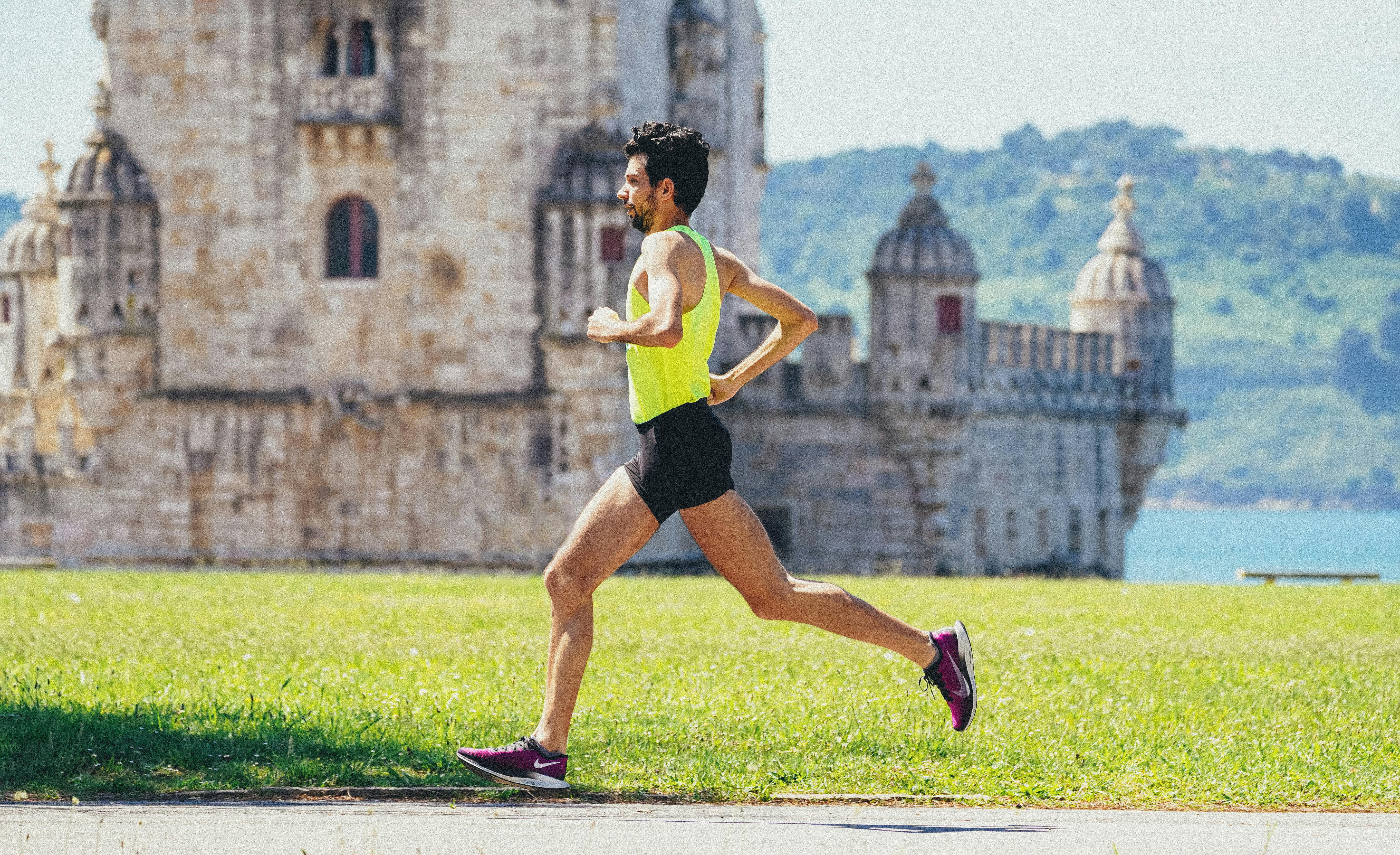 Fit young male jogger running along embankment of lake · Free Stock Photo