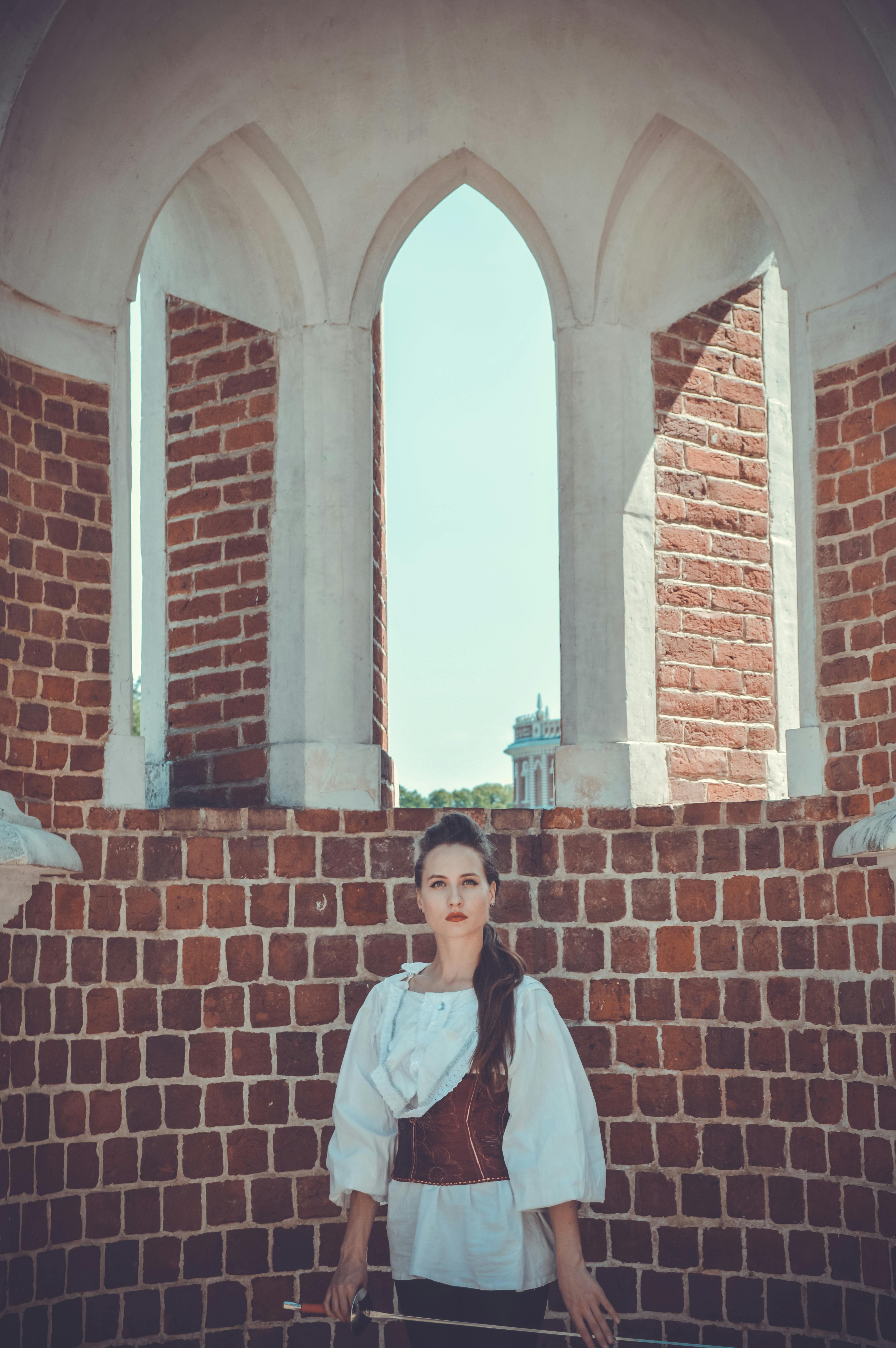 Serious young female standing in medieval stone castle on sunny day ...