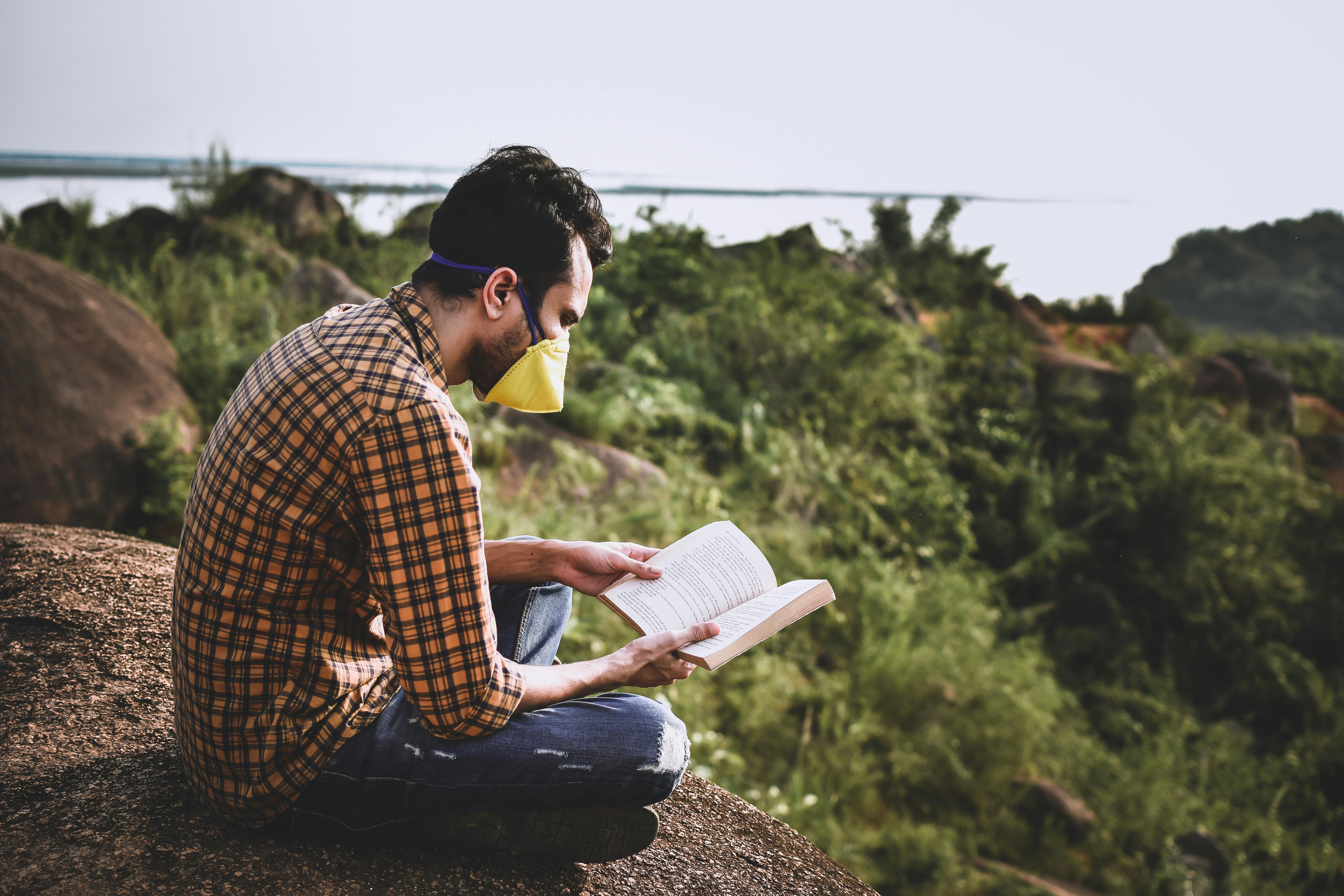 A Man Sitting on the Rock while Reading a Book · Free Stock Photo