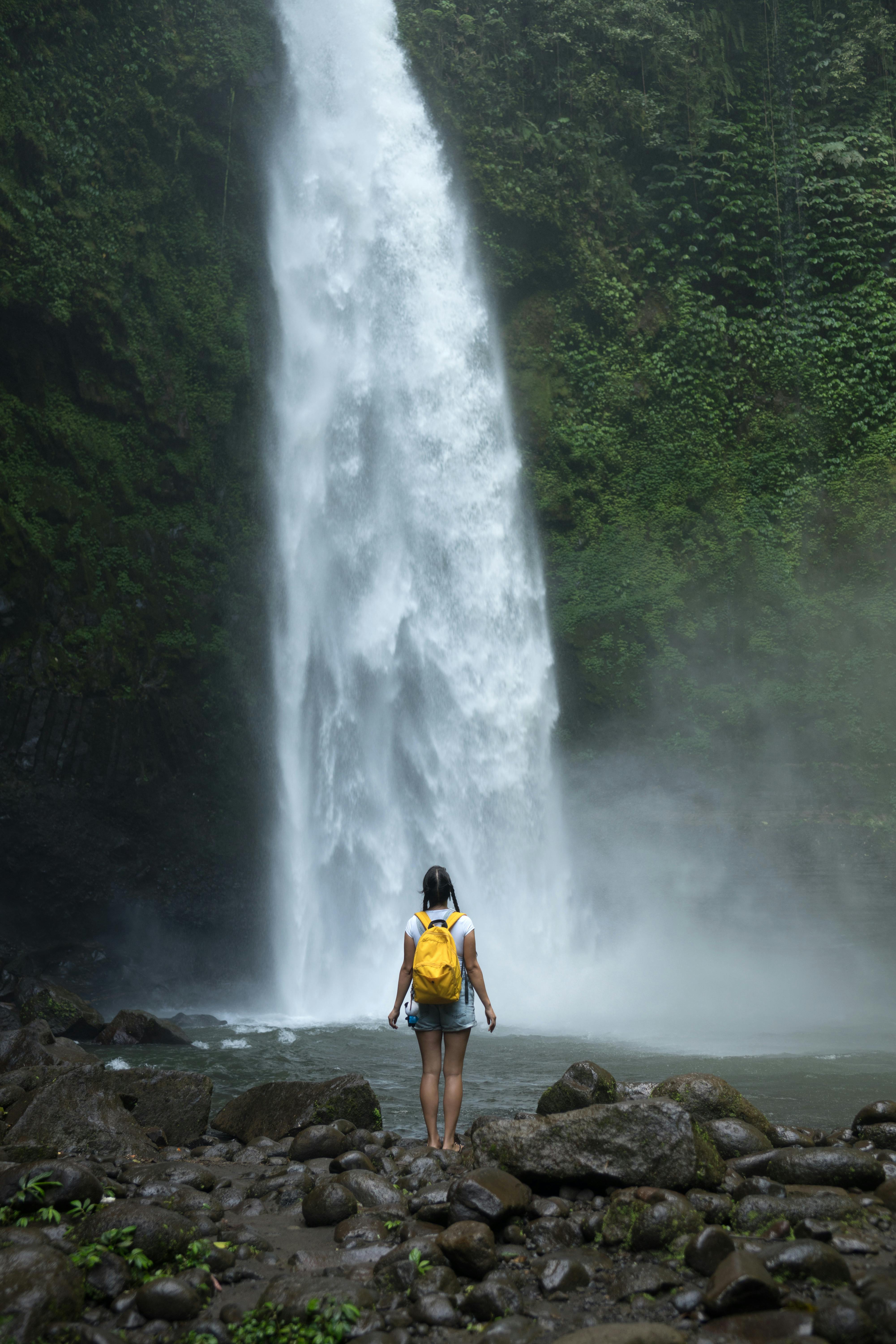 Back View of a Woman Standing on Rocks near the Waterfalls · Free Stock ...