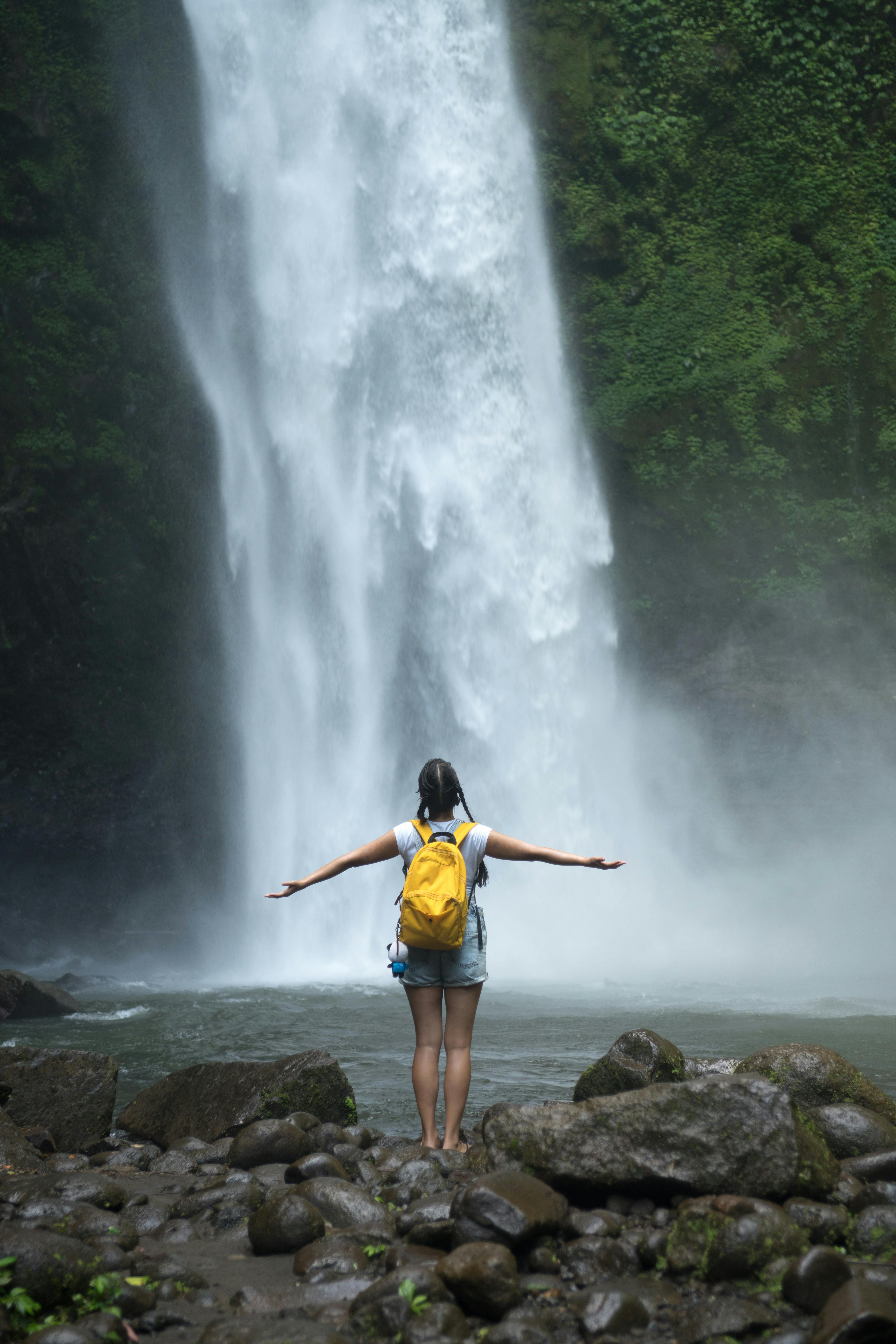 Relaxed woman with outstretched arms admiring waterfall · Free Stock Photo