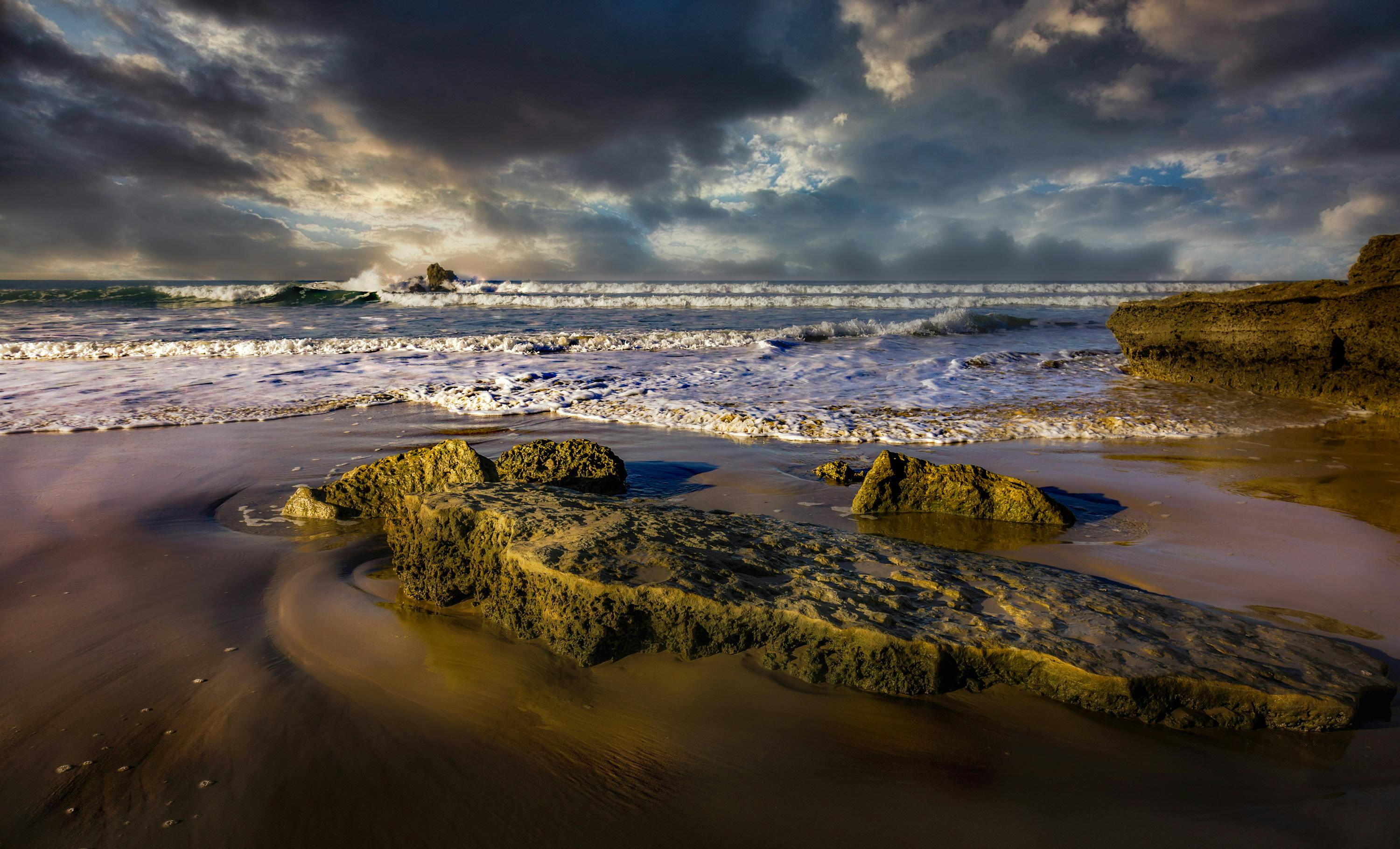 Rocks in stormy ocean under gloomy sky at sunset · Free Stock Photo
