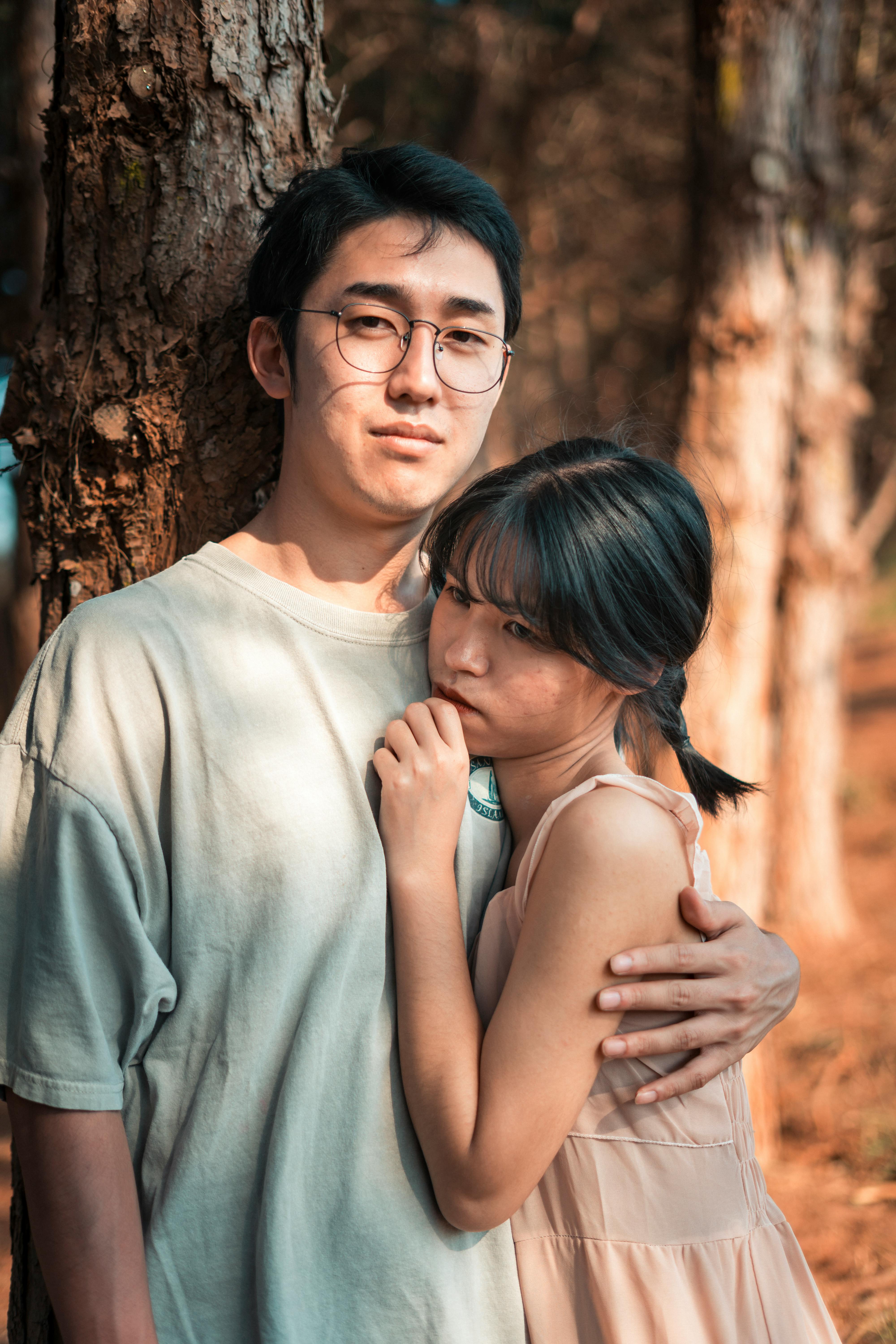 Asian couple hugging near tree trunk · Free Stock Photo