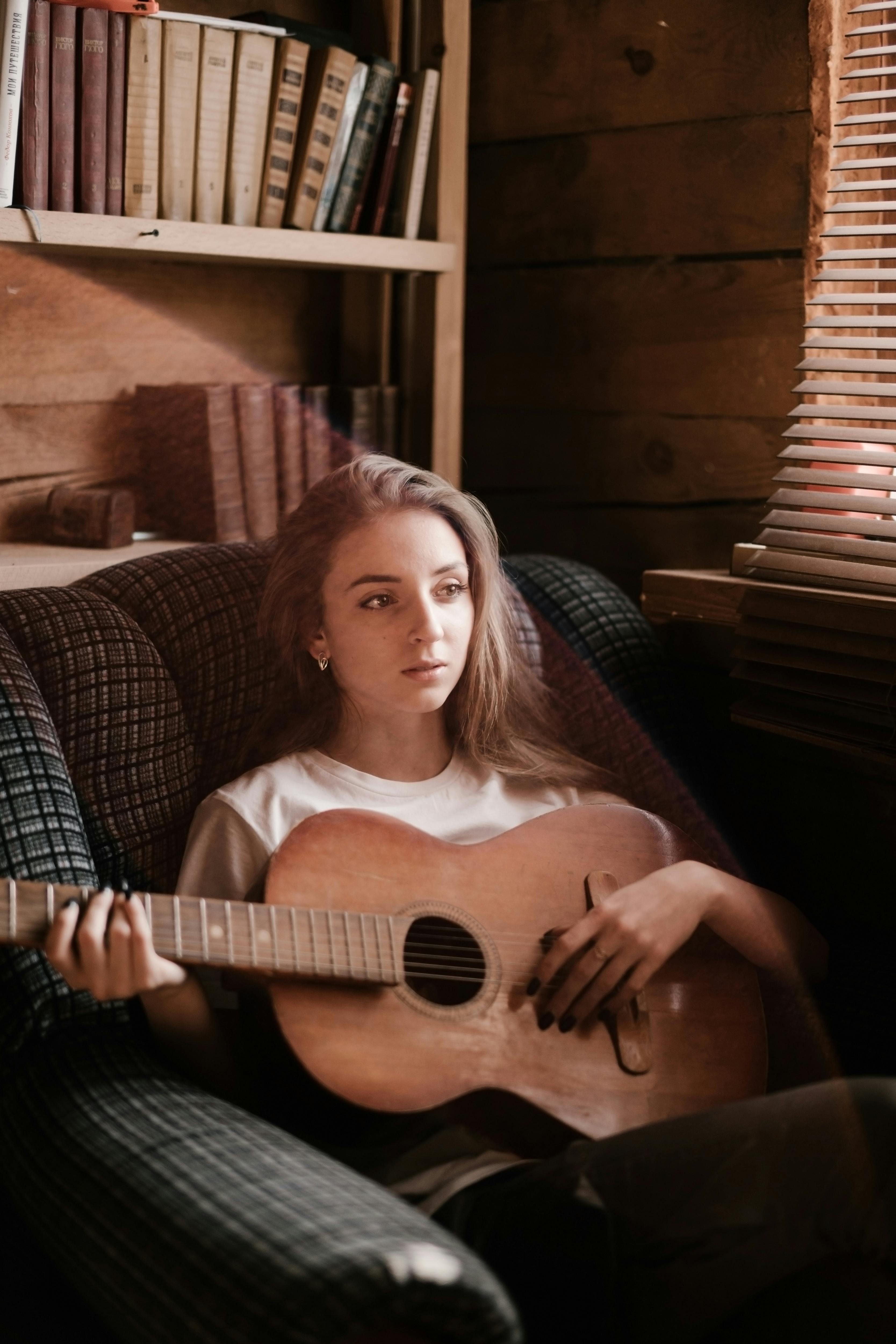Woman Sitting in Armchair Playing Guitar · Free Stock Photo