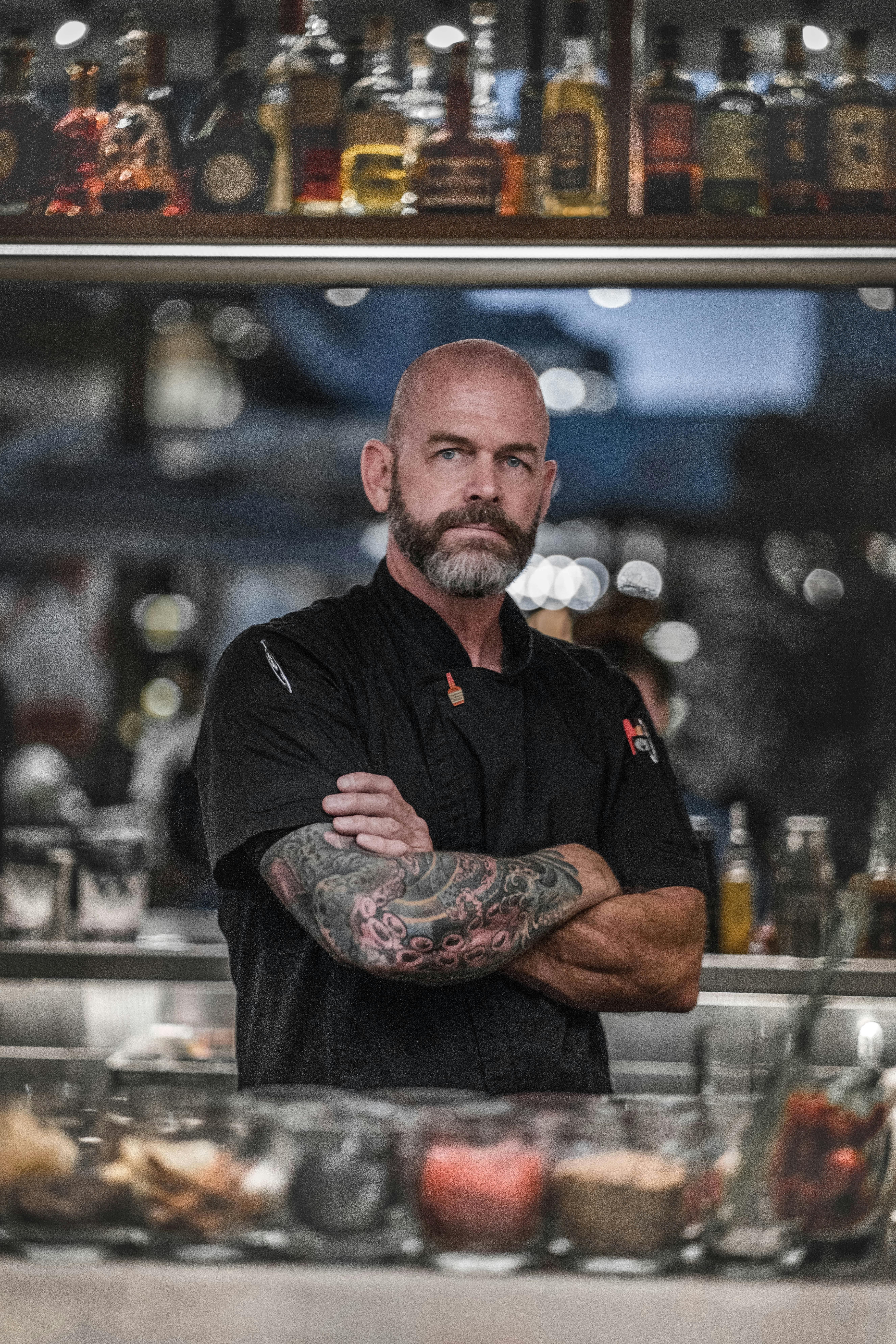 Bartender with Tattoos Standing Behind a Bar · Free Stock Photo