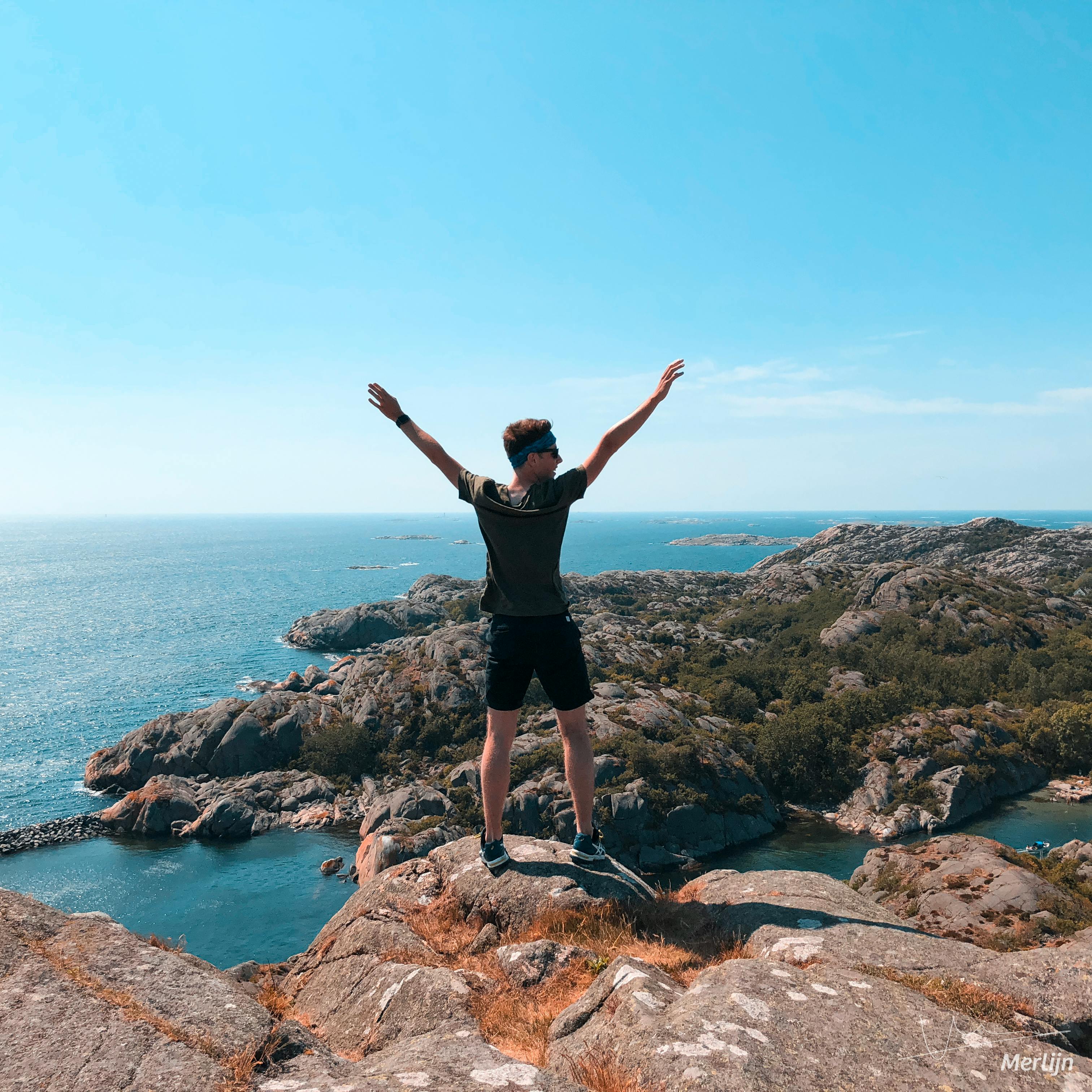 Back View of a Man Standing on Rocks Raising His Hands · Free Stock Photo