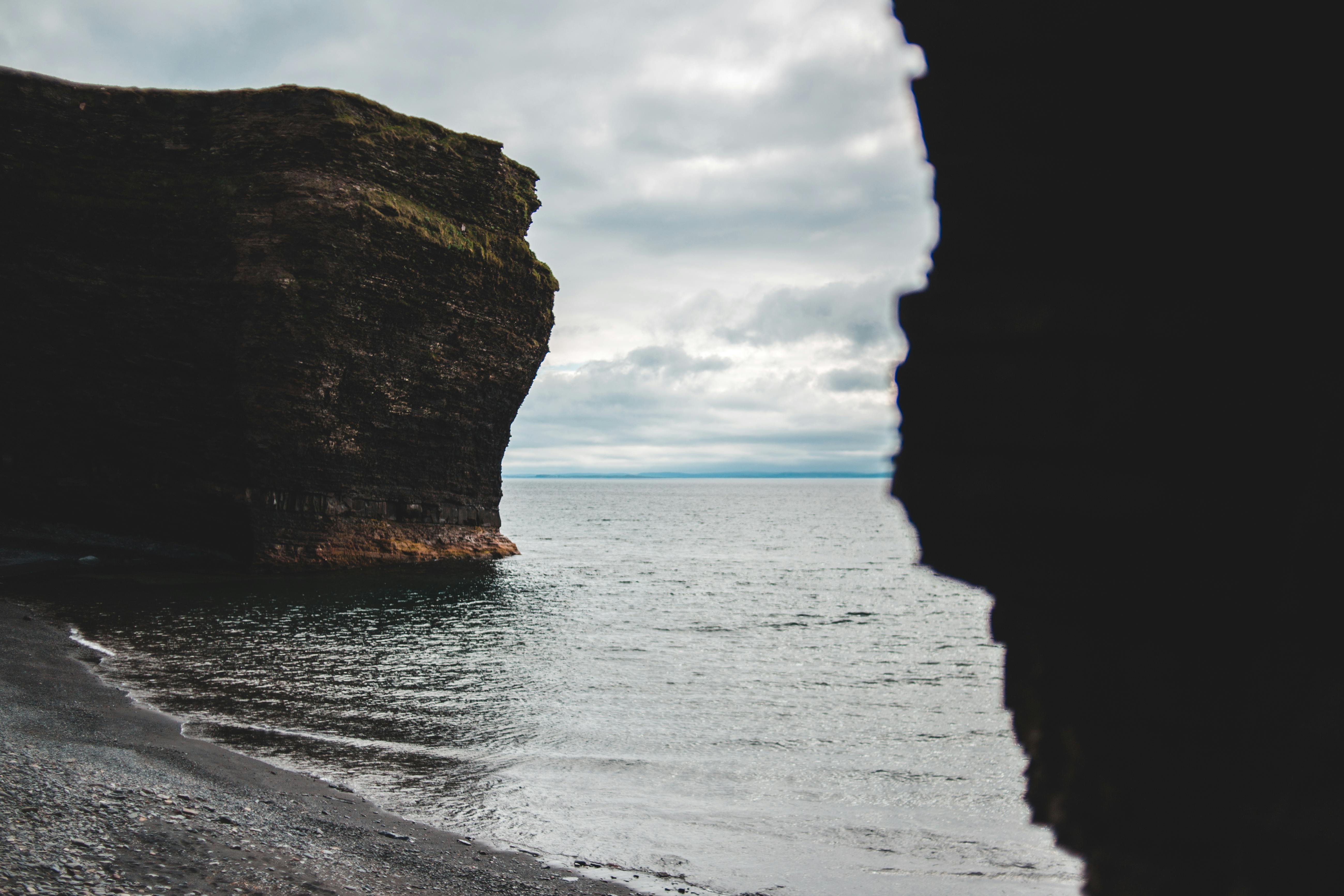 Calm shore with walkway and cliff arch · Free Stock Photo