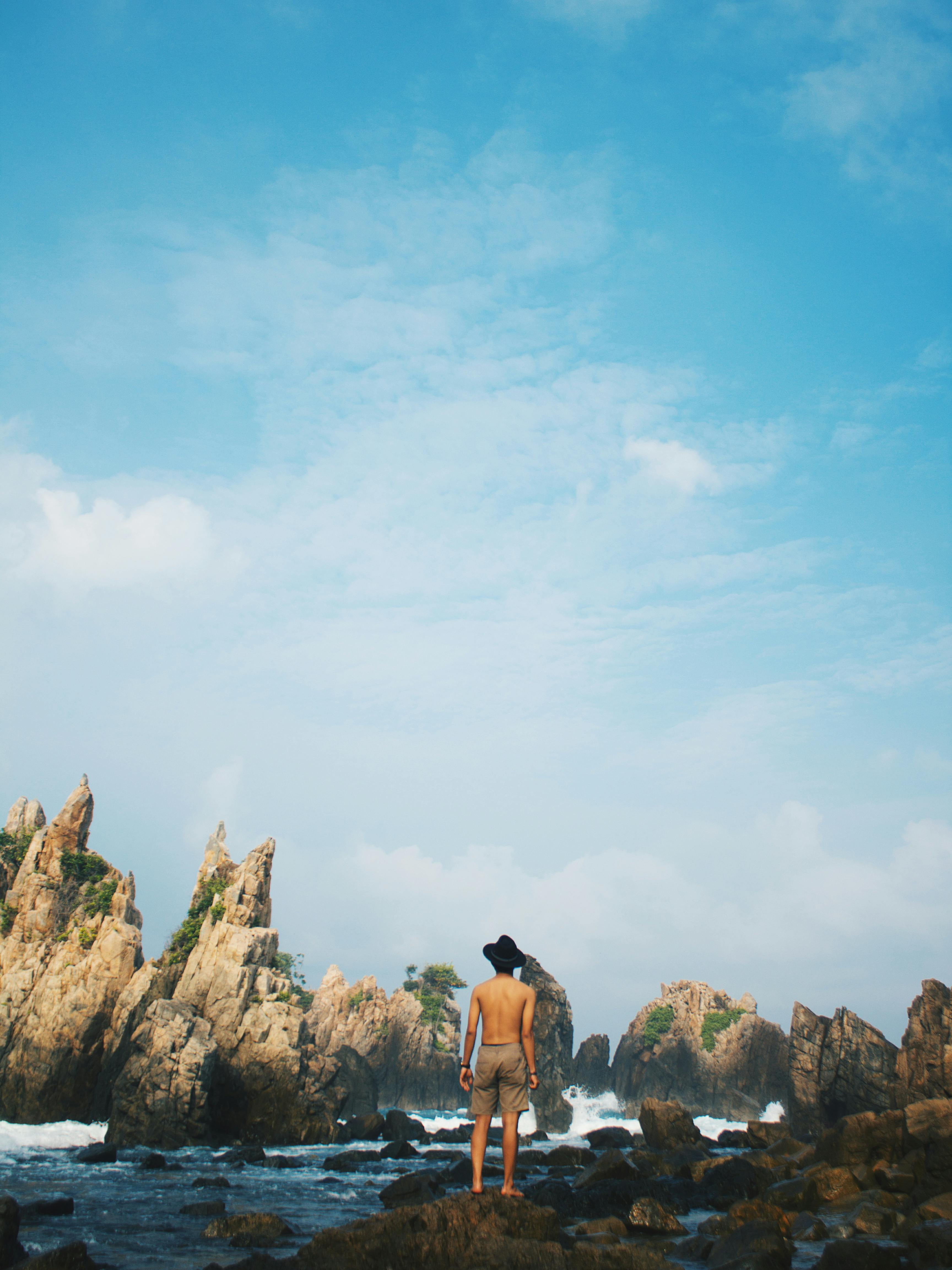 Back View of a Man Standing on Rocks Raising His Hands · Free Stock Photo