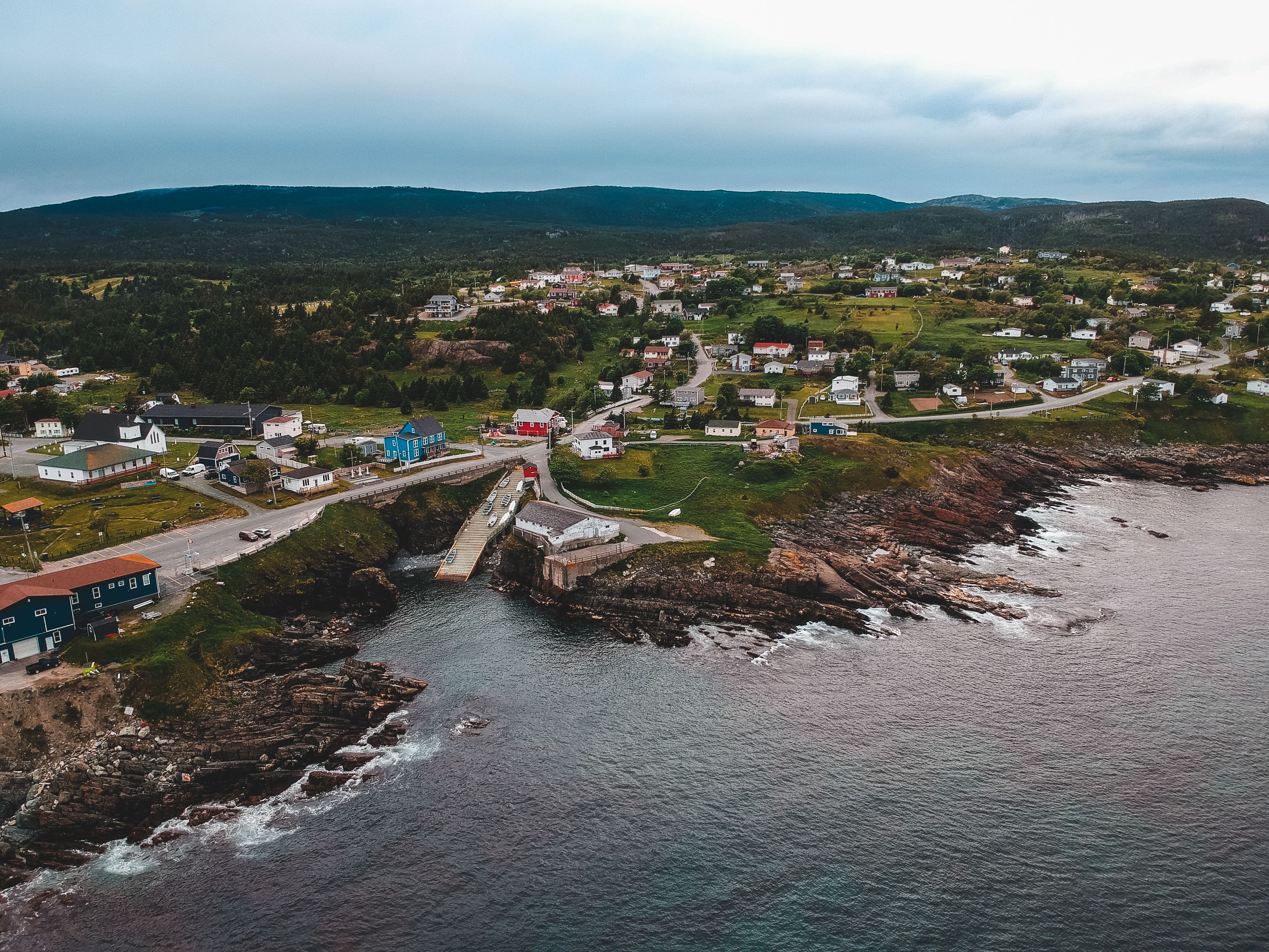 Sea near mountains and residential houses in countryside · Free Stock Photo