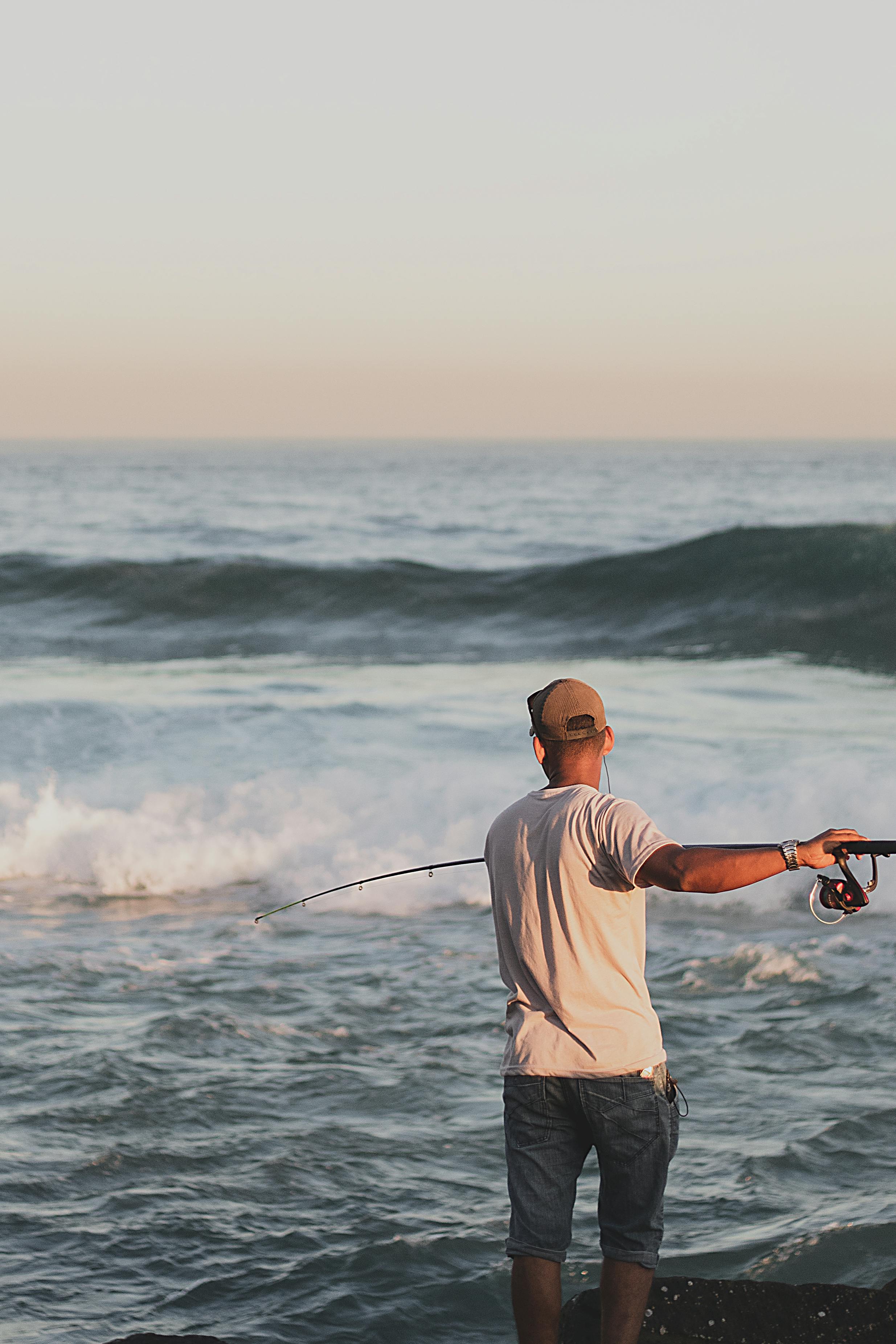 Anonymous fisherman catching fish on ocean in evening · Free Stock Photo