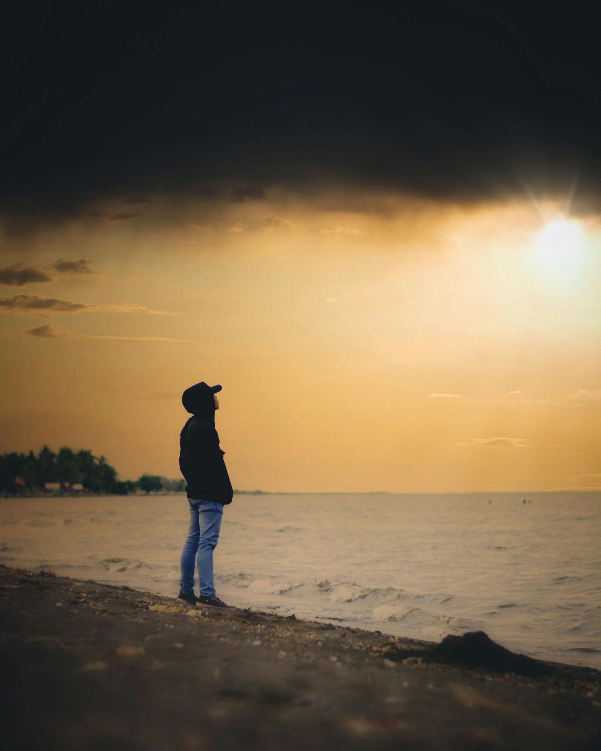 Man in Hoodie Jacket Standing on Beach during Sunset · Free Stock Photo