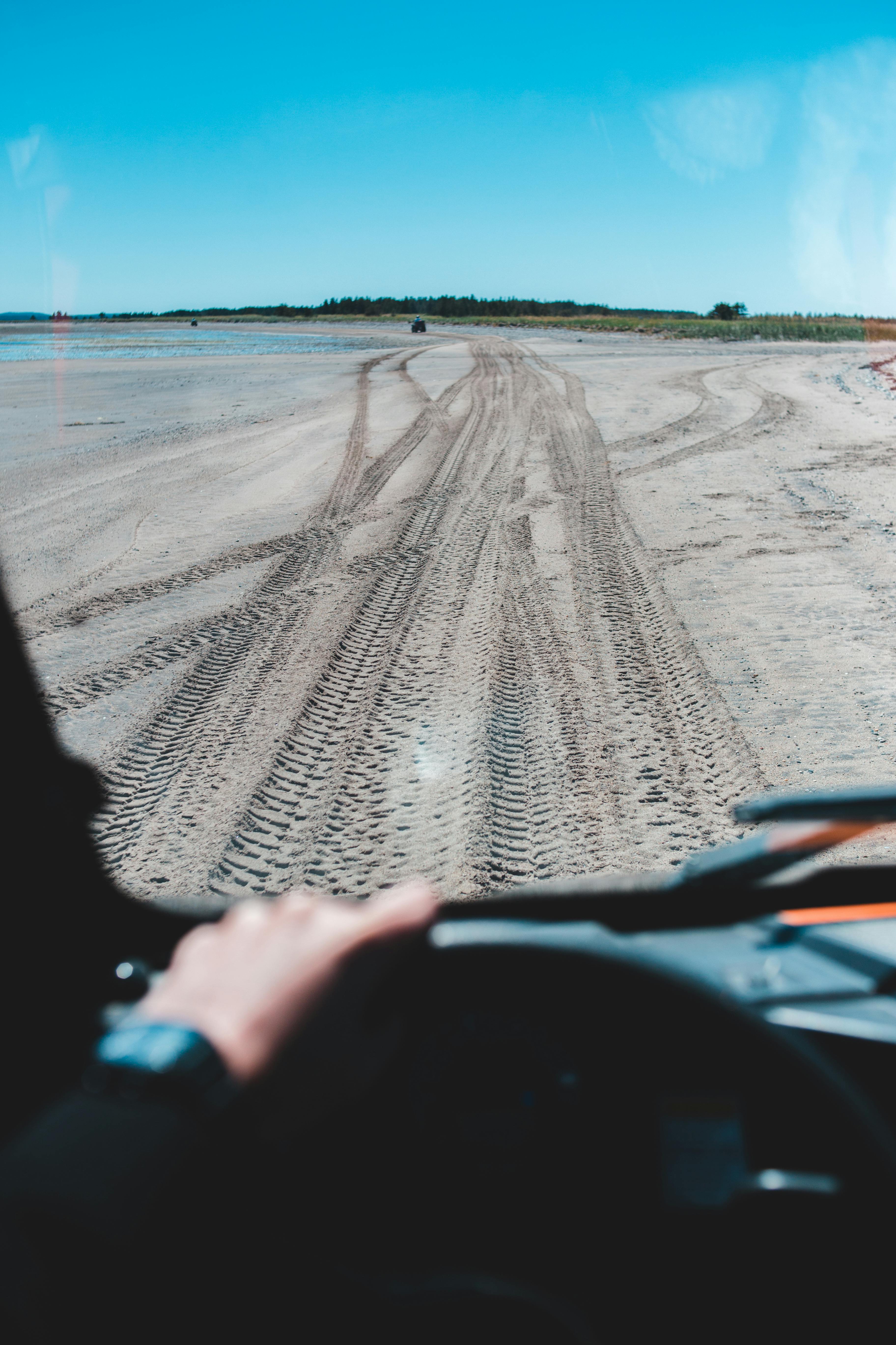 Faceless driver in vehicle on sandy walkway with traces · Free Stock Photo